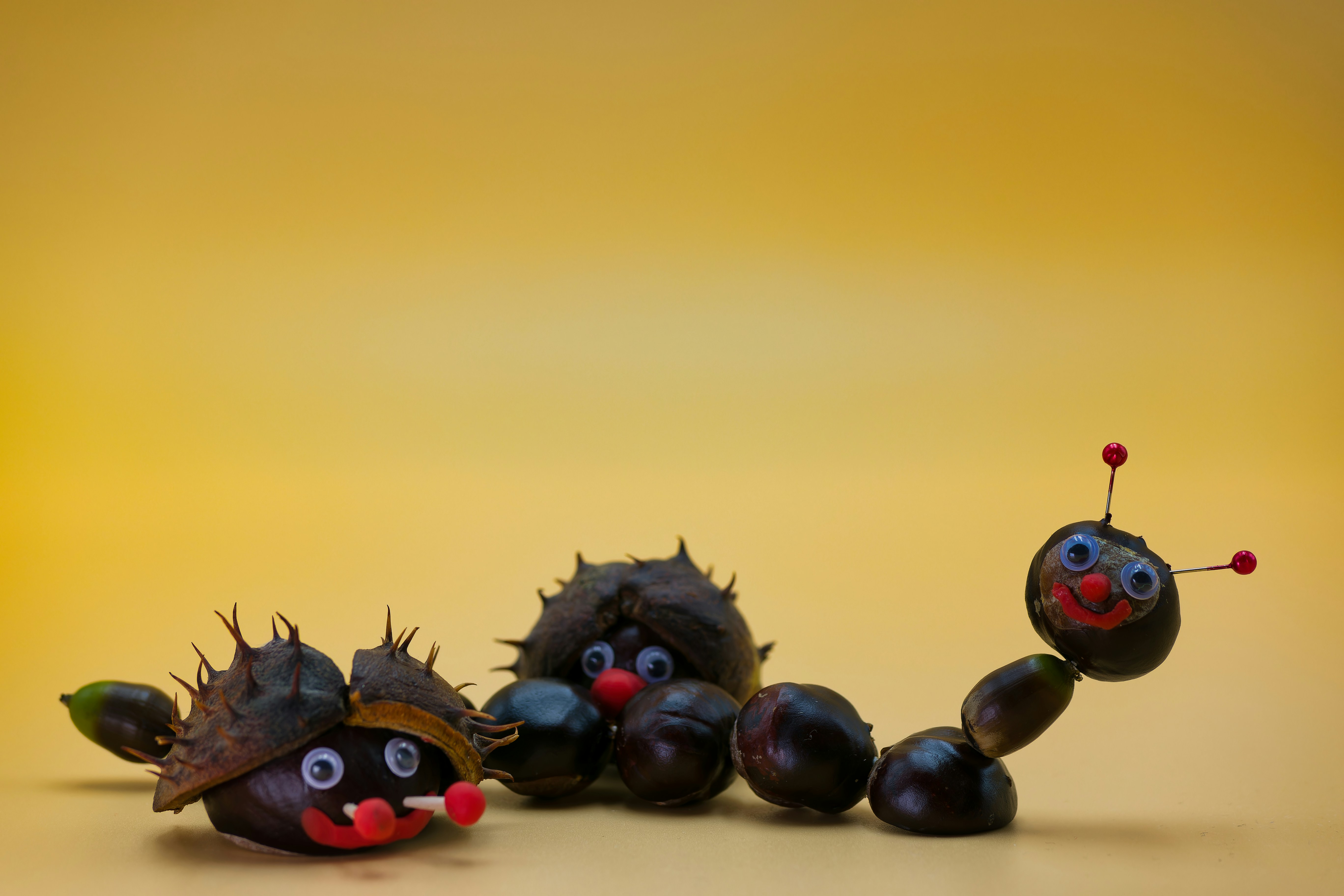 Three glossy berries with smiley faces sit on a yellow surface, forming a whimsical little parade against a soft, warm backdrop. This is a candid still-life with small character accents.