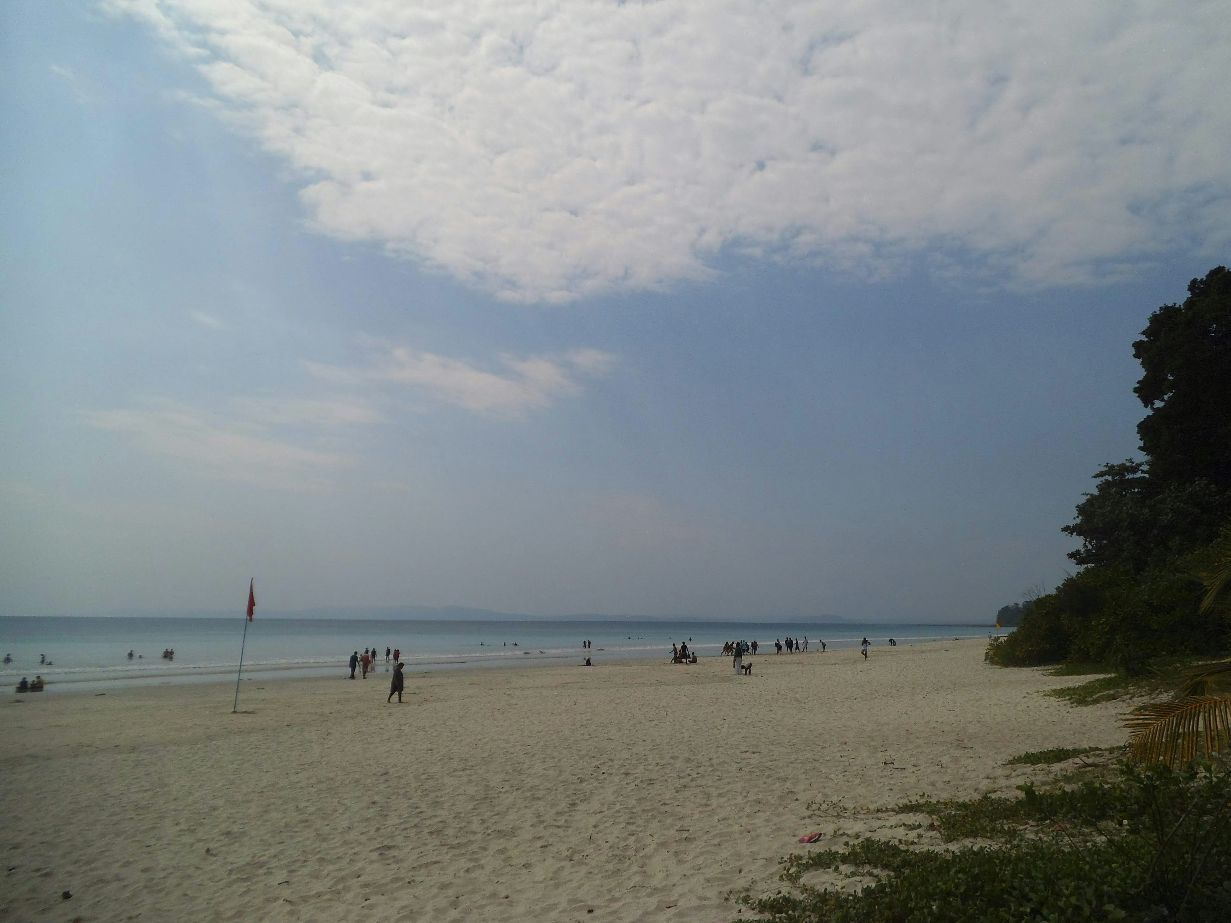 Flag and Distant Silhouettes: A Quiet Coastal Day Unfolds Along the Beach