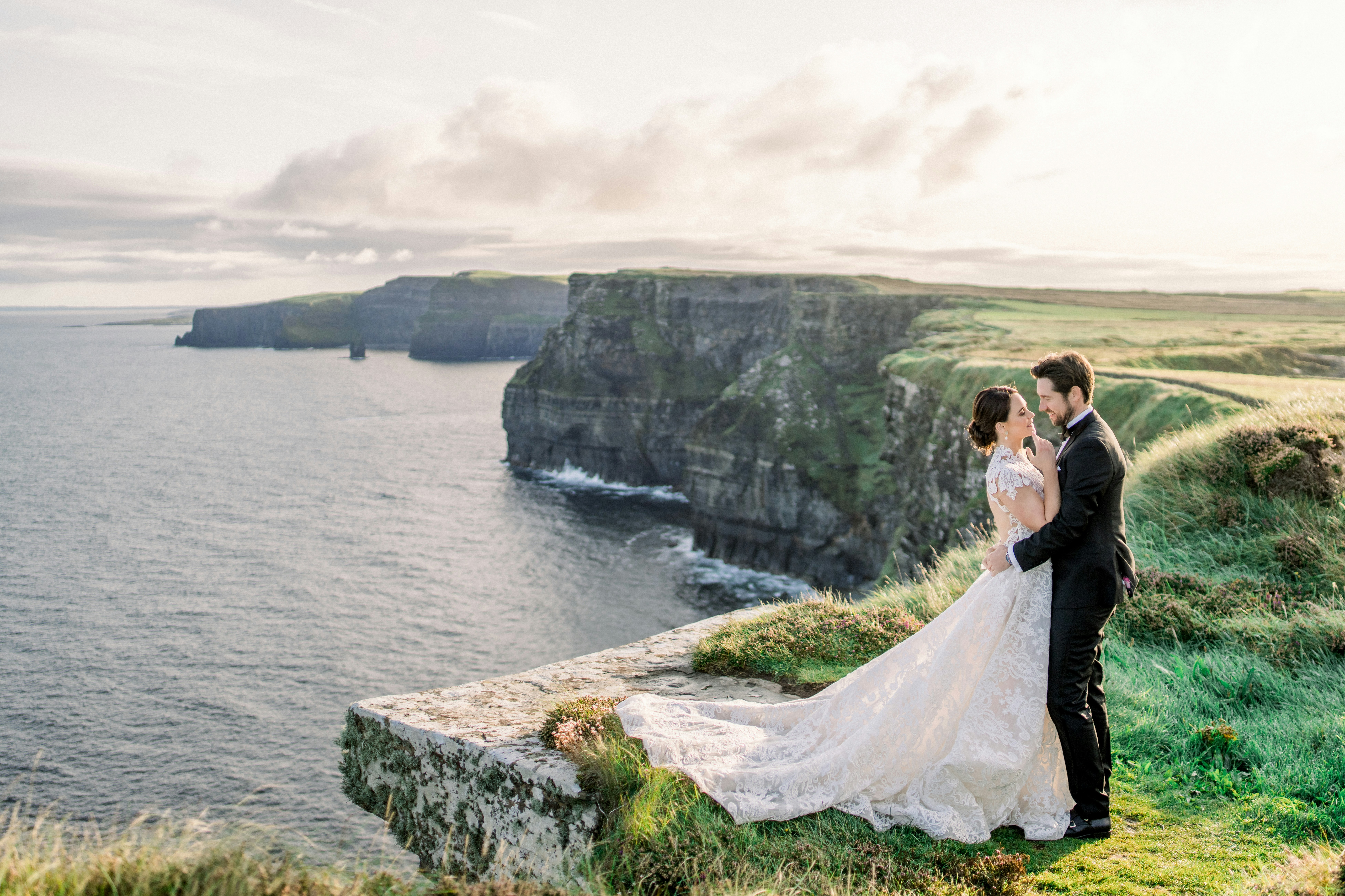 A bride and groom standing on a cliff overlooking the ocean photo ...