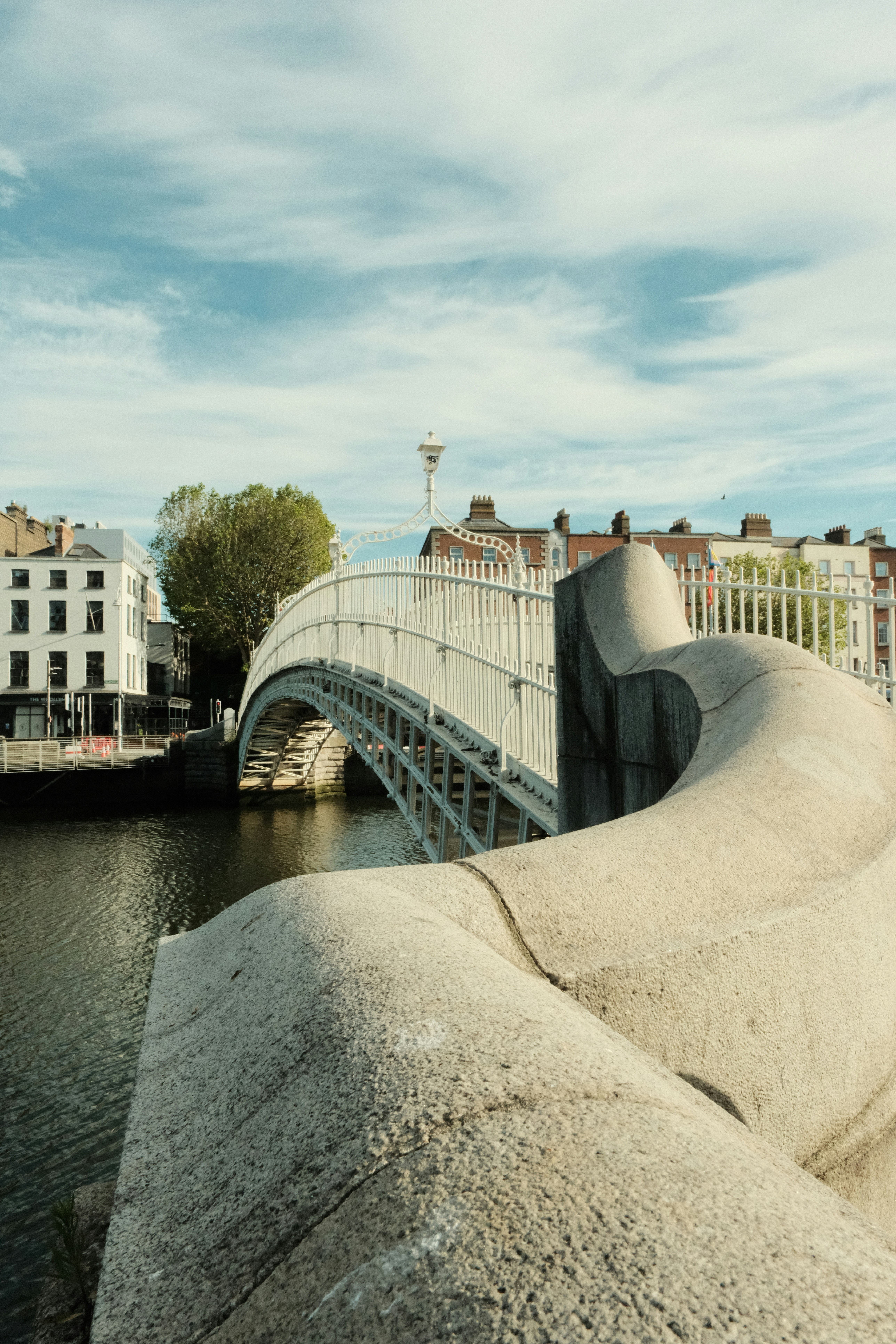 Sunlit Curves Over the River: A White Pedestrian Bridge Framed by Stone and Sky