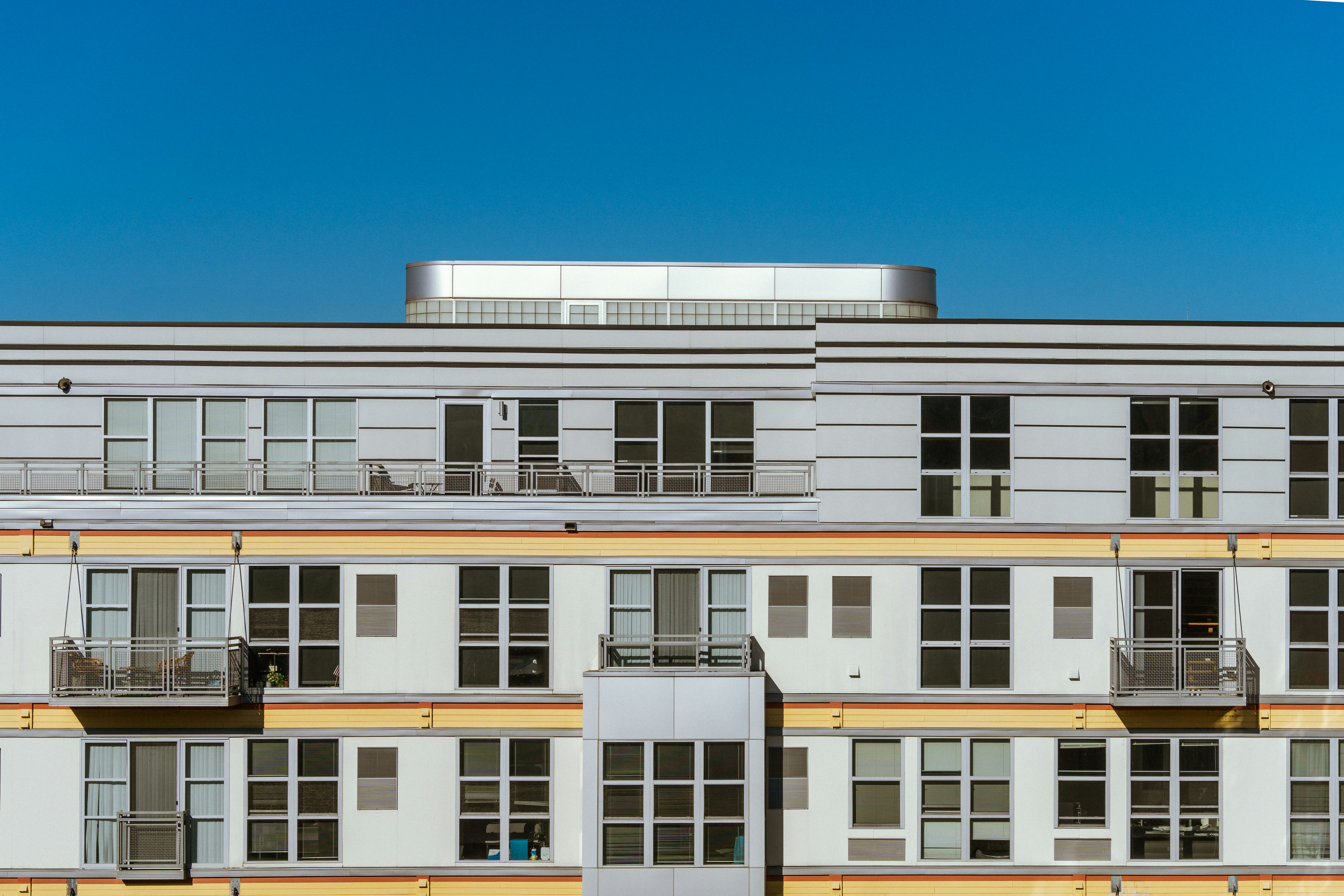 Illustration of a modern building with multiple windows and balconies against a clear blue sky.