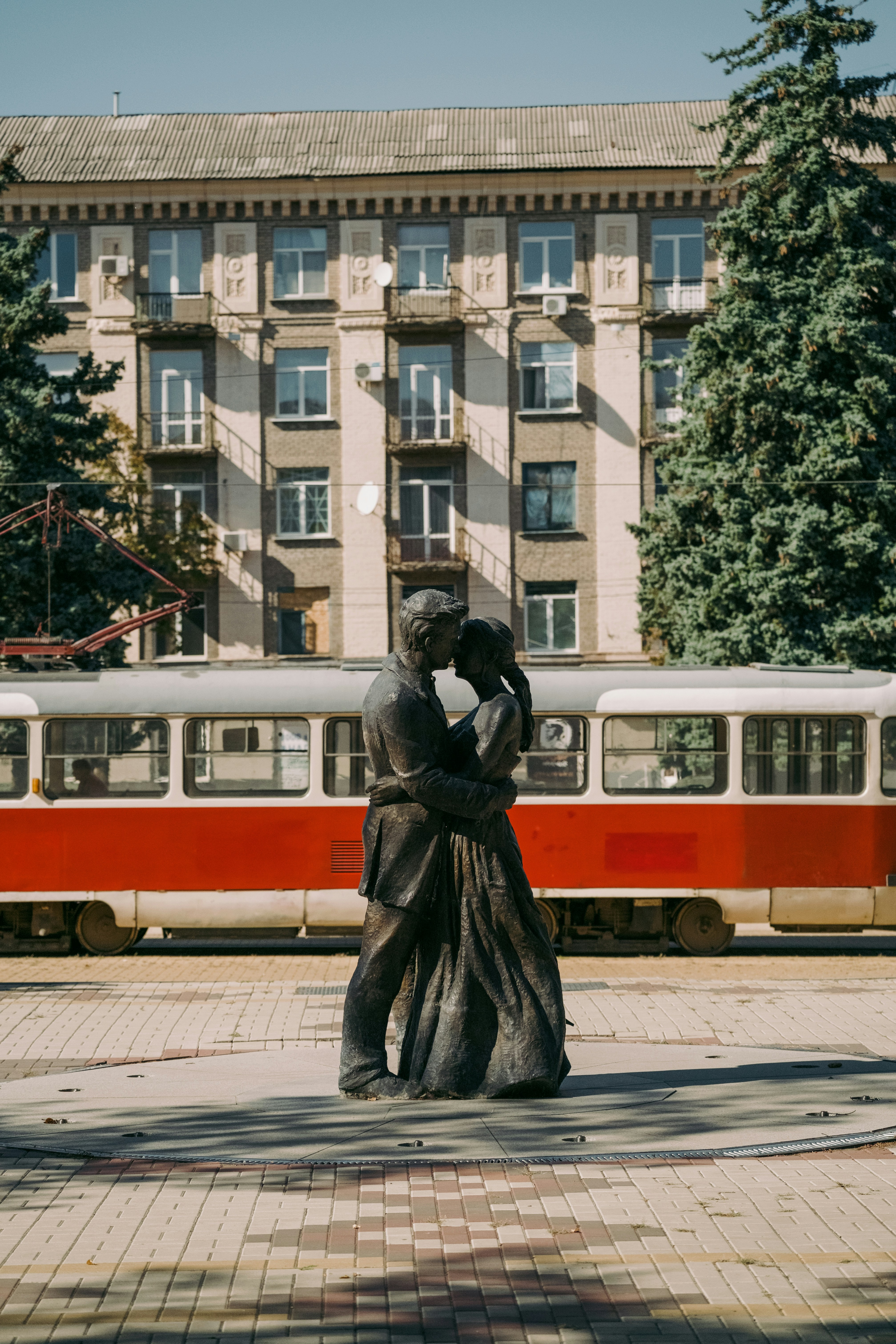 Bronze Lovers in the City Pause: A Red Tram, a Facade, and the Moment Between