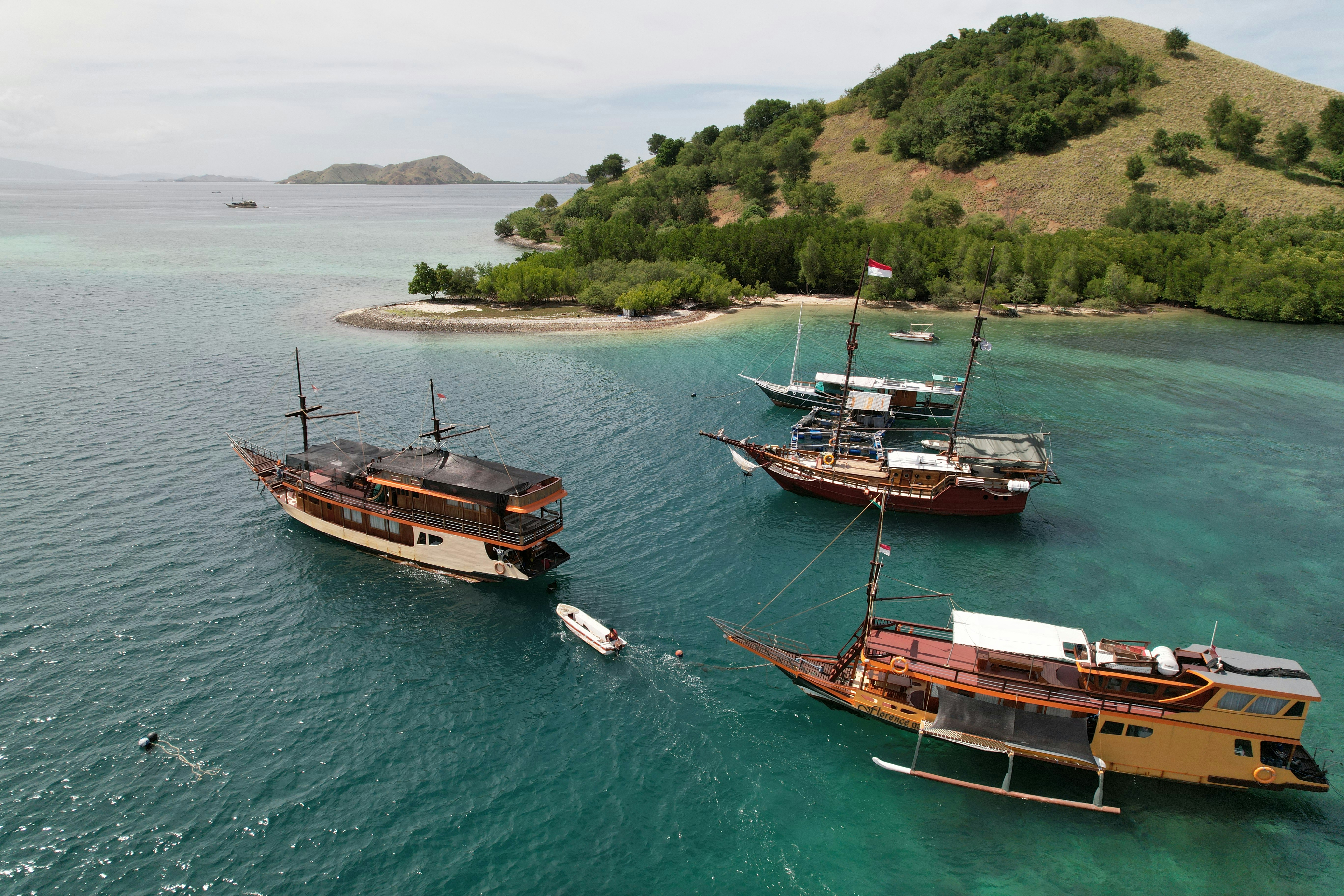 Four boats anchored in crystal-clear waters, surrounded by lush greenery and a serene coastline. The scene captures the essence of maritime tranquility.