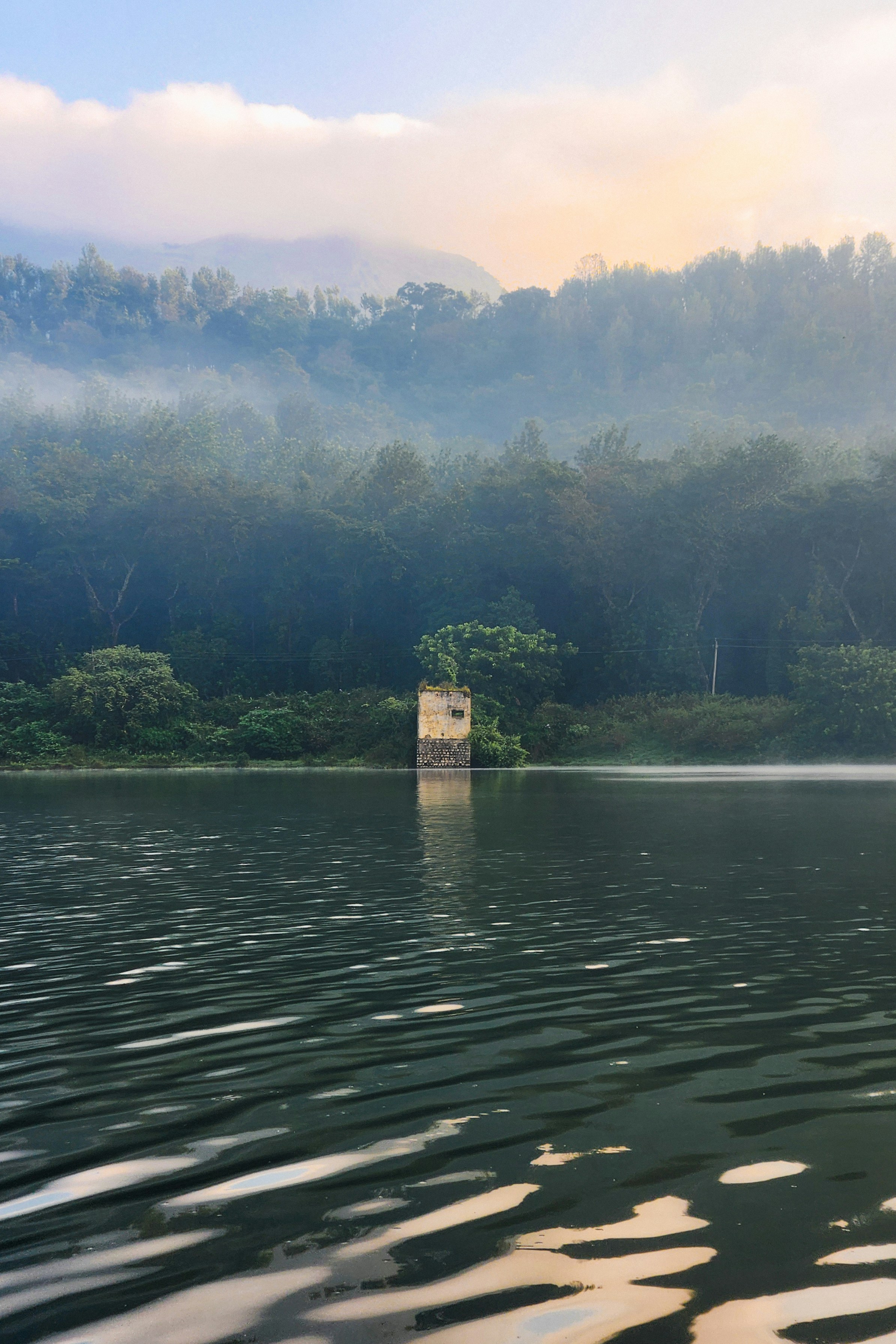 A misty lake in Chikkamagaluru surrounded by dense forest and rolling hills, where calm water reflections and soft morning light capture the serene beauty of the Western Ghats.