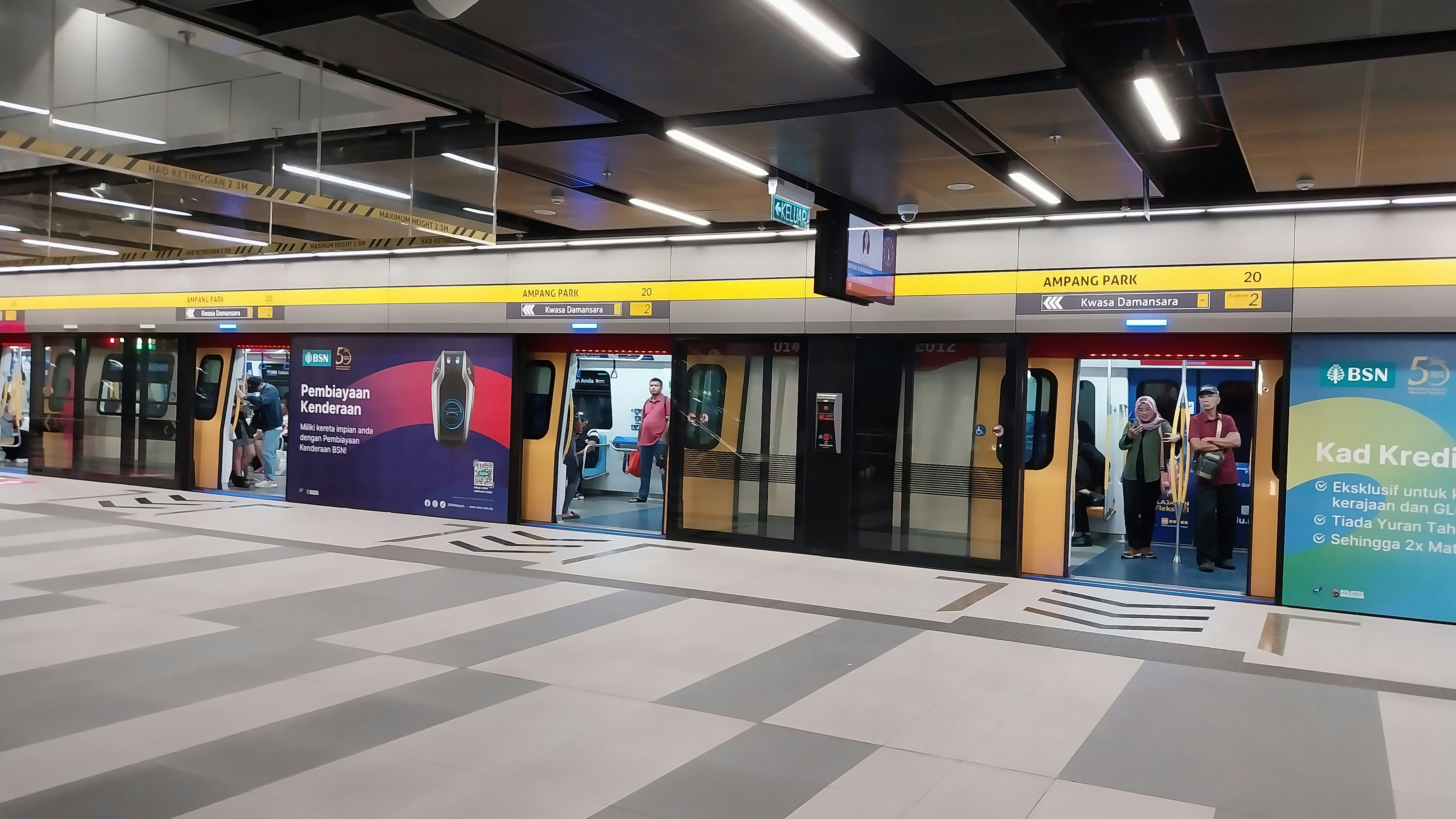 Subway platform with yellow-accented train doors and advertising banners along the wall; empty tracks extend into the foreground, suggesting a calm moment in a bustling station.