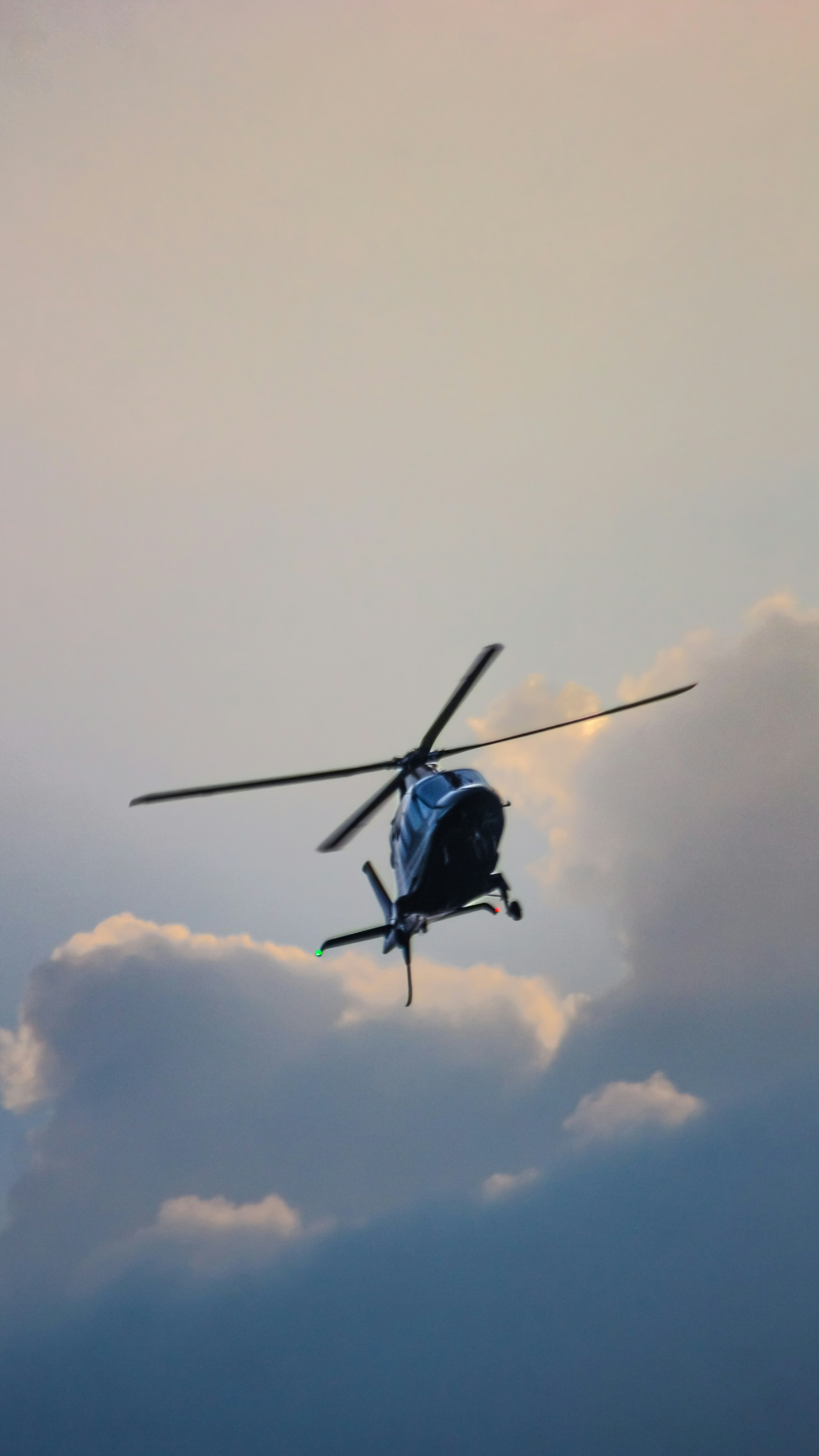A helicopter glides gracefully against a backdrop of soft, pastel clouds during twilight.