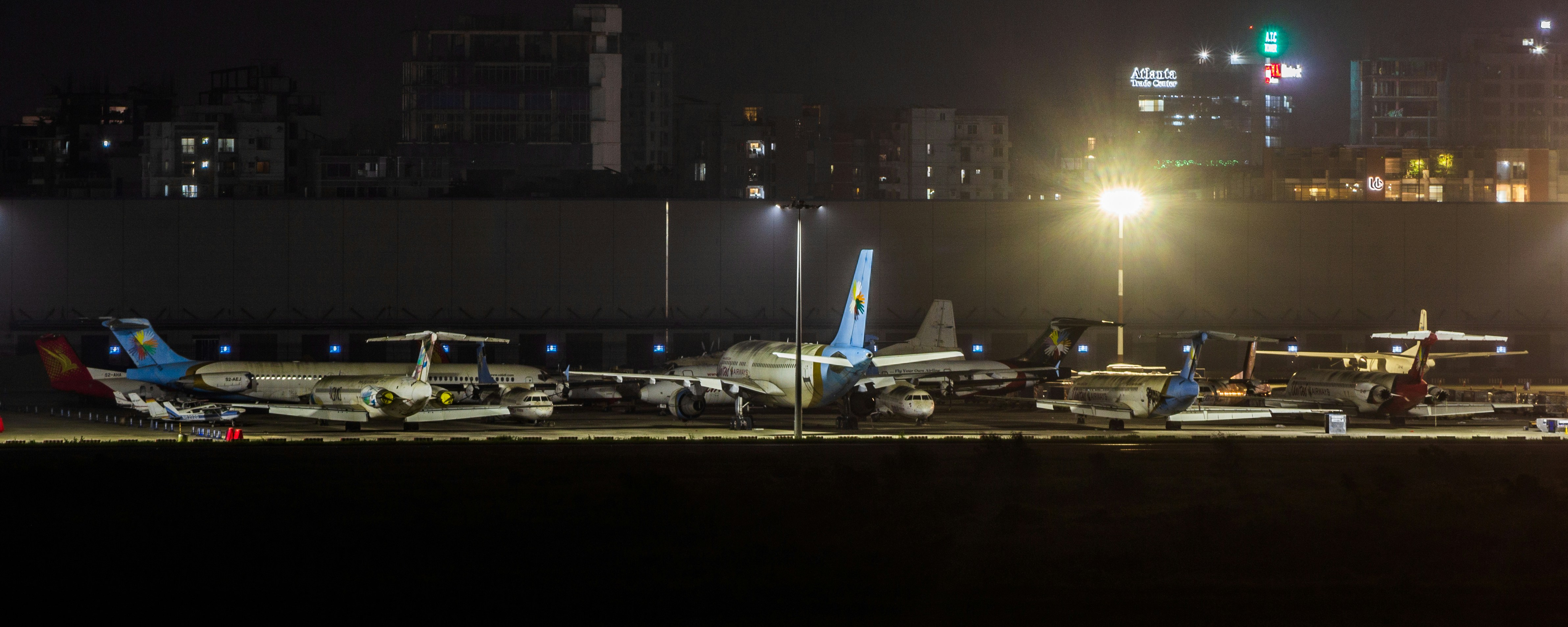 A collection of vintage aircraft illuminated by artificial lights at night, showcasing their unique designs against a dark urban backdrop.