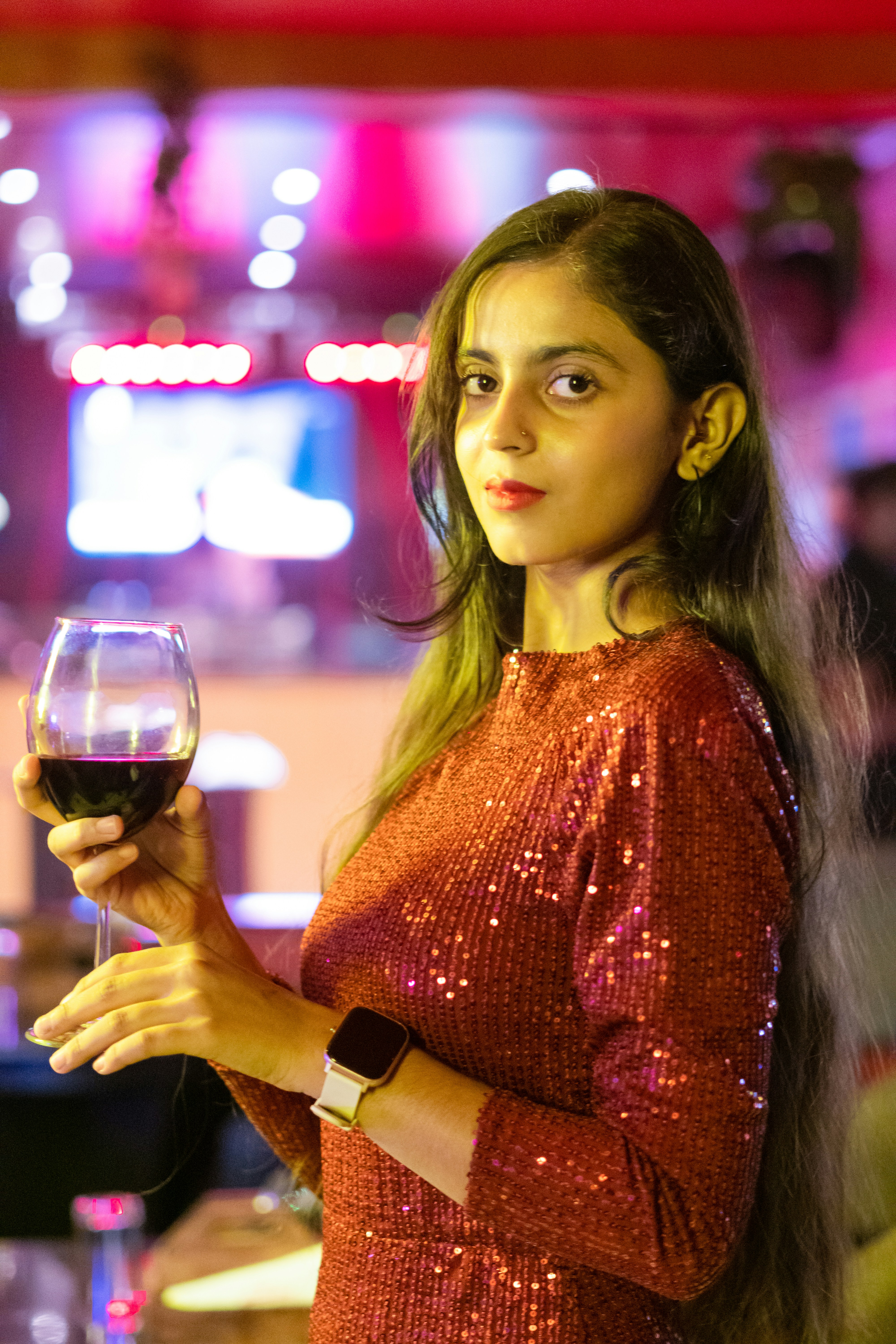Teen girl in red gown with wine glass in bar.