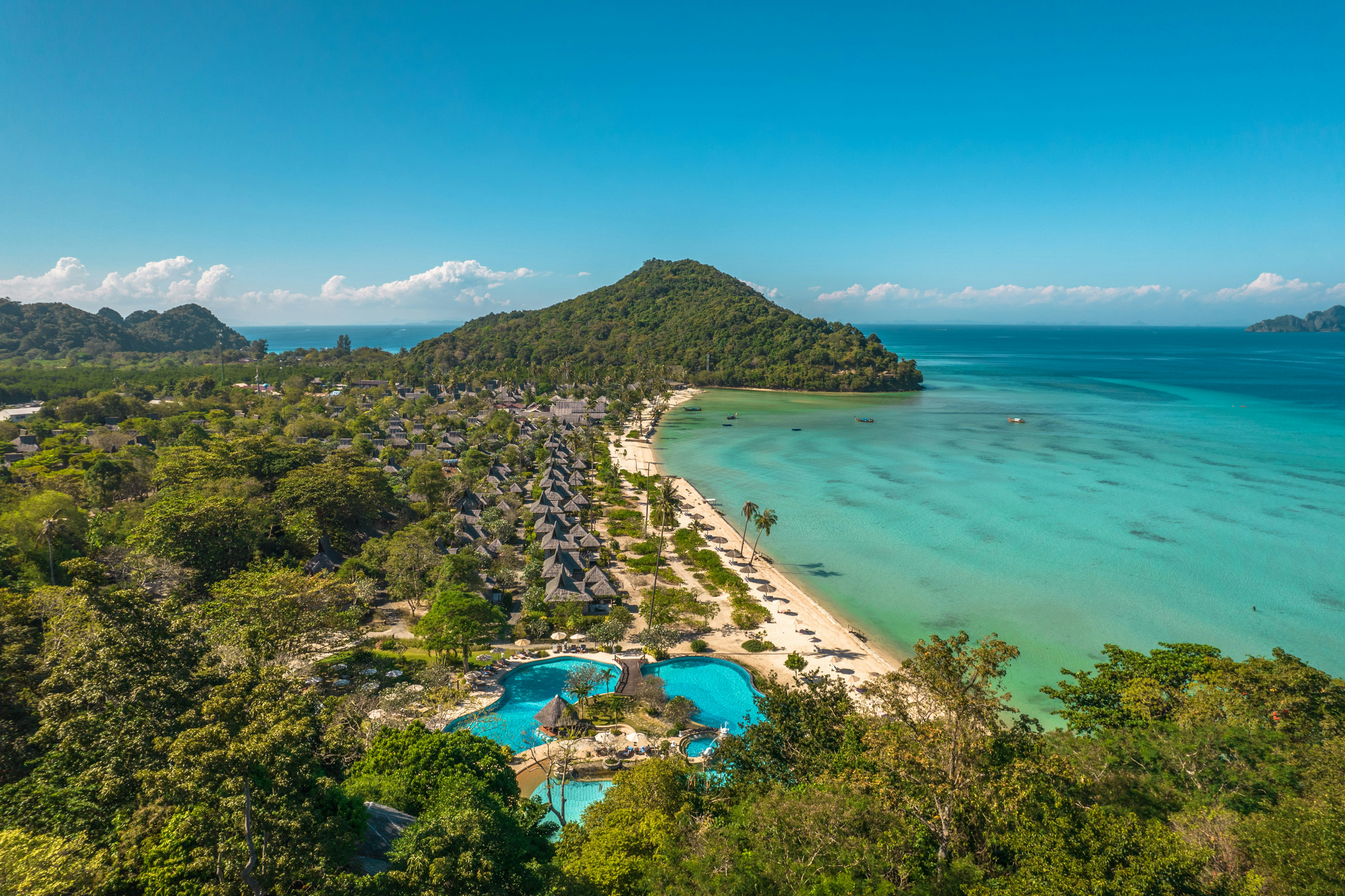 Aerial view of a tranquil beach resort nestled between lush greenery and turquoise waters, showcasing a blend of nature and luxury.