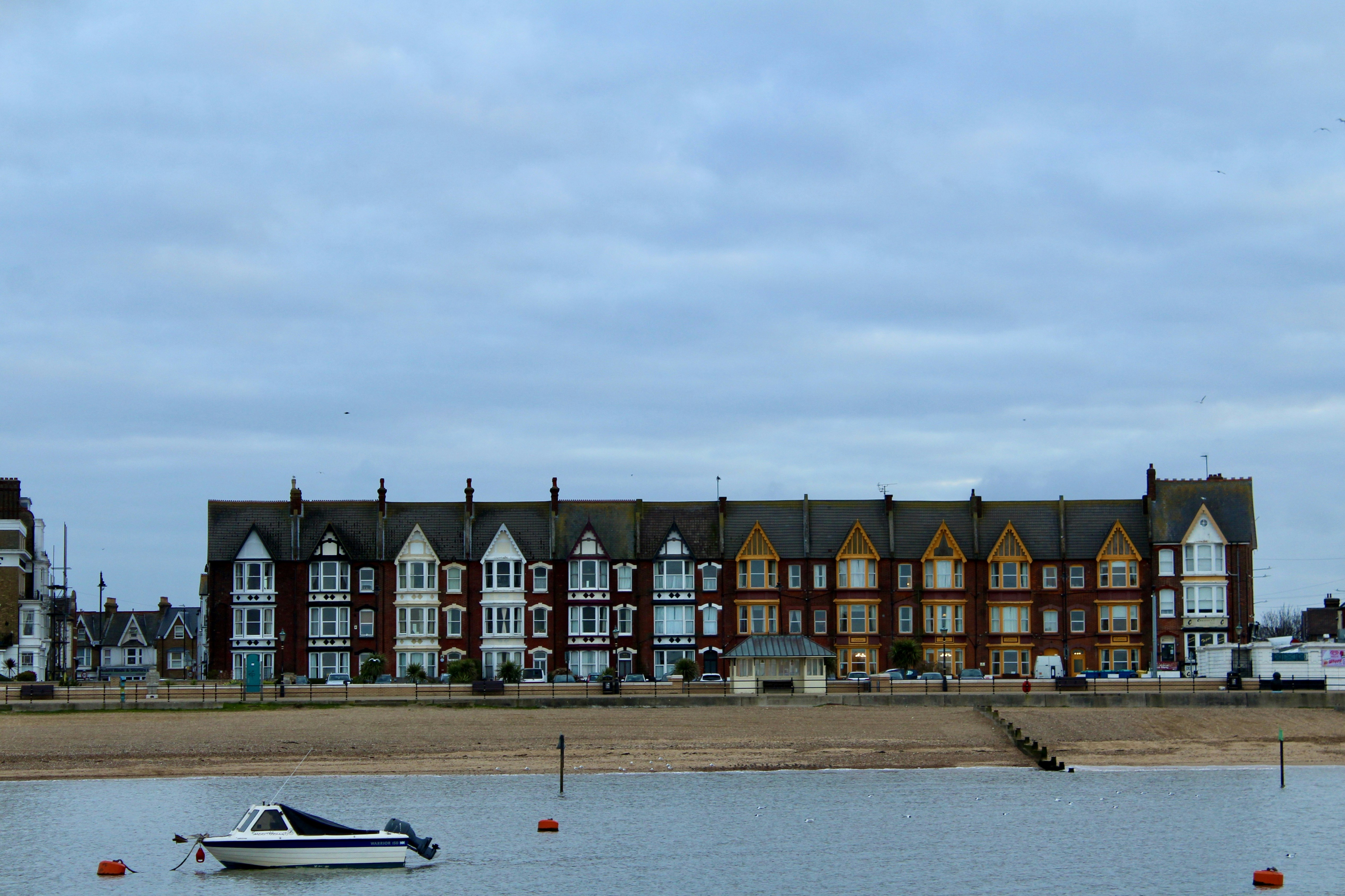 Row of colorful townhouses by a tranquil seaside under a cloudy sky.
