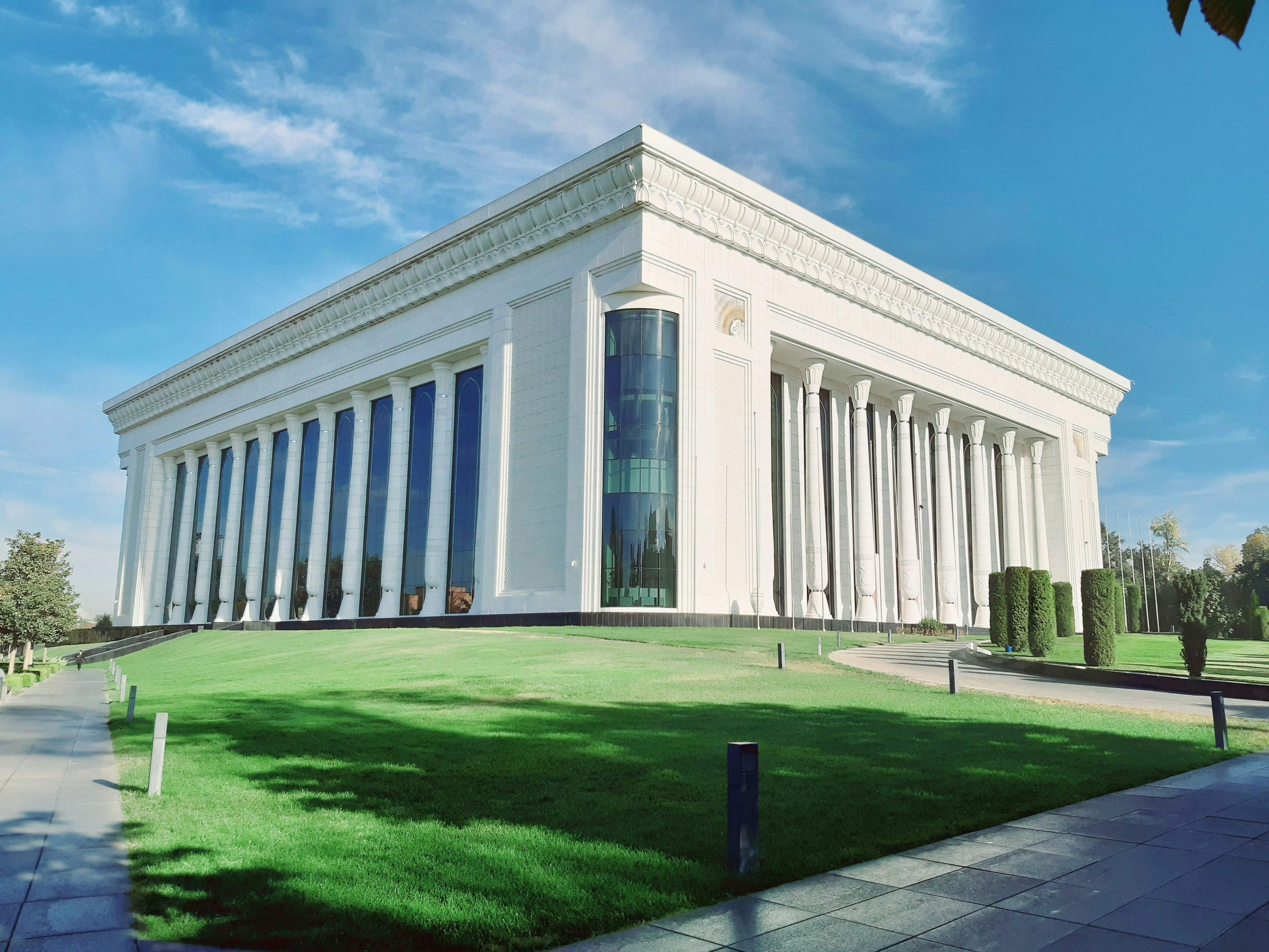 Large white neoclassical building with tall columns on a vibrant green lawn under a clear blue sky.