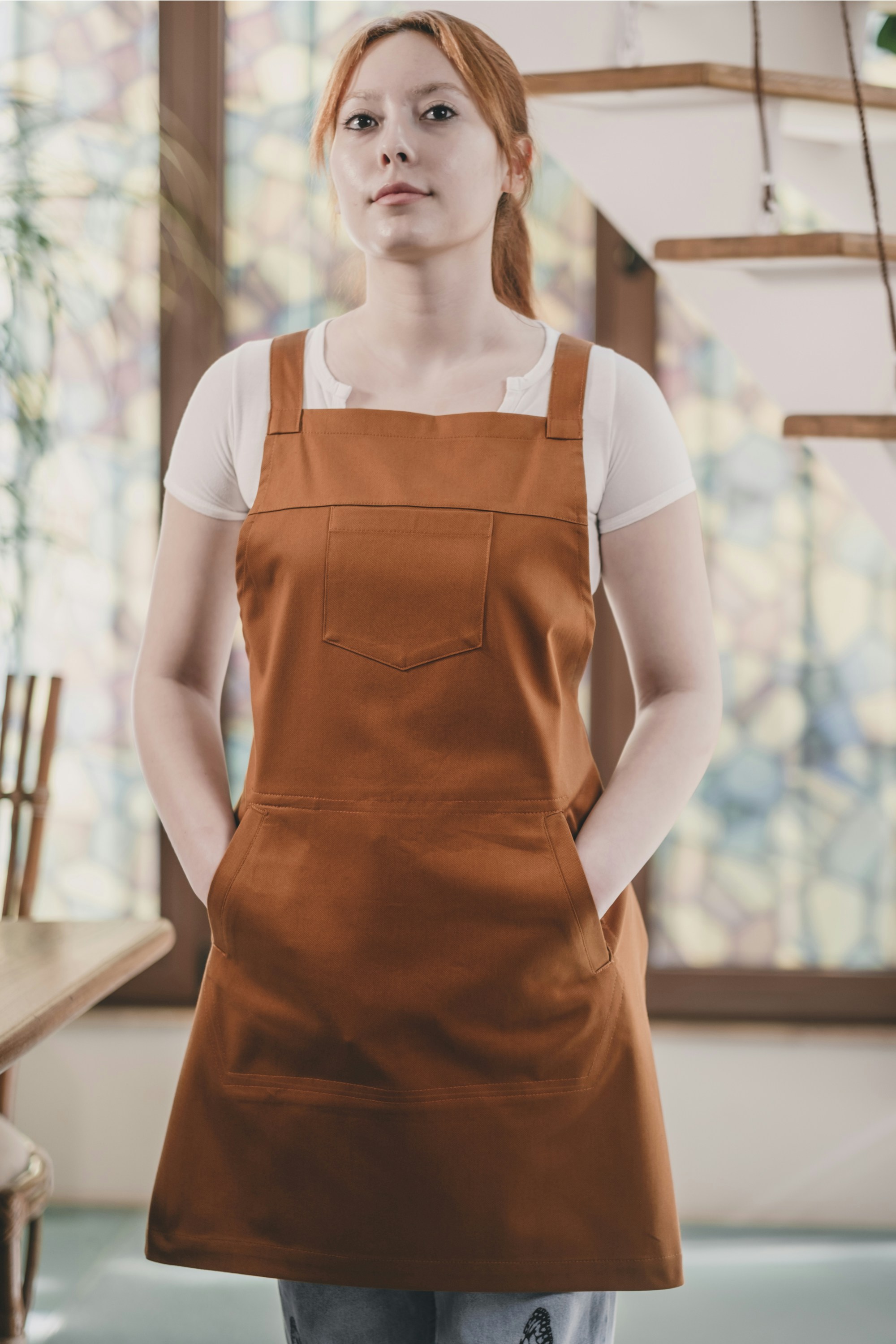 A woman in an orange apron standing in front of a stained glass window ...