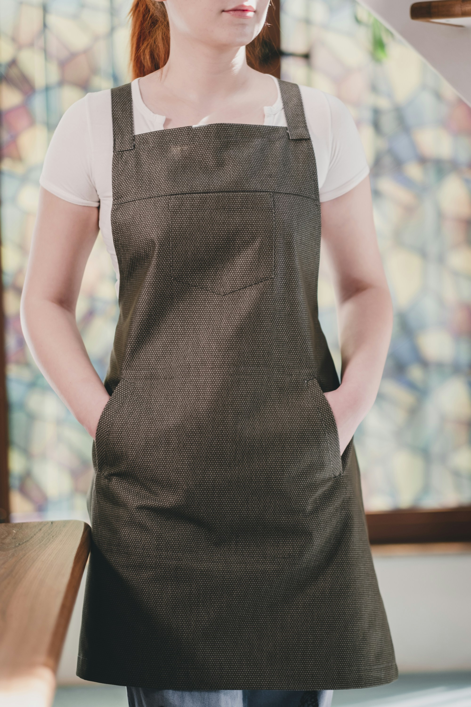 A woman wearing an apron standing in front of a stained glass window ...