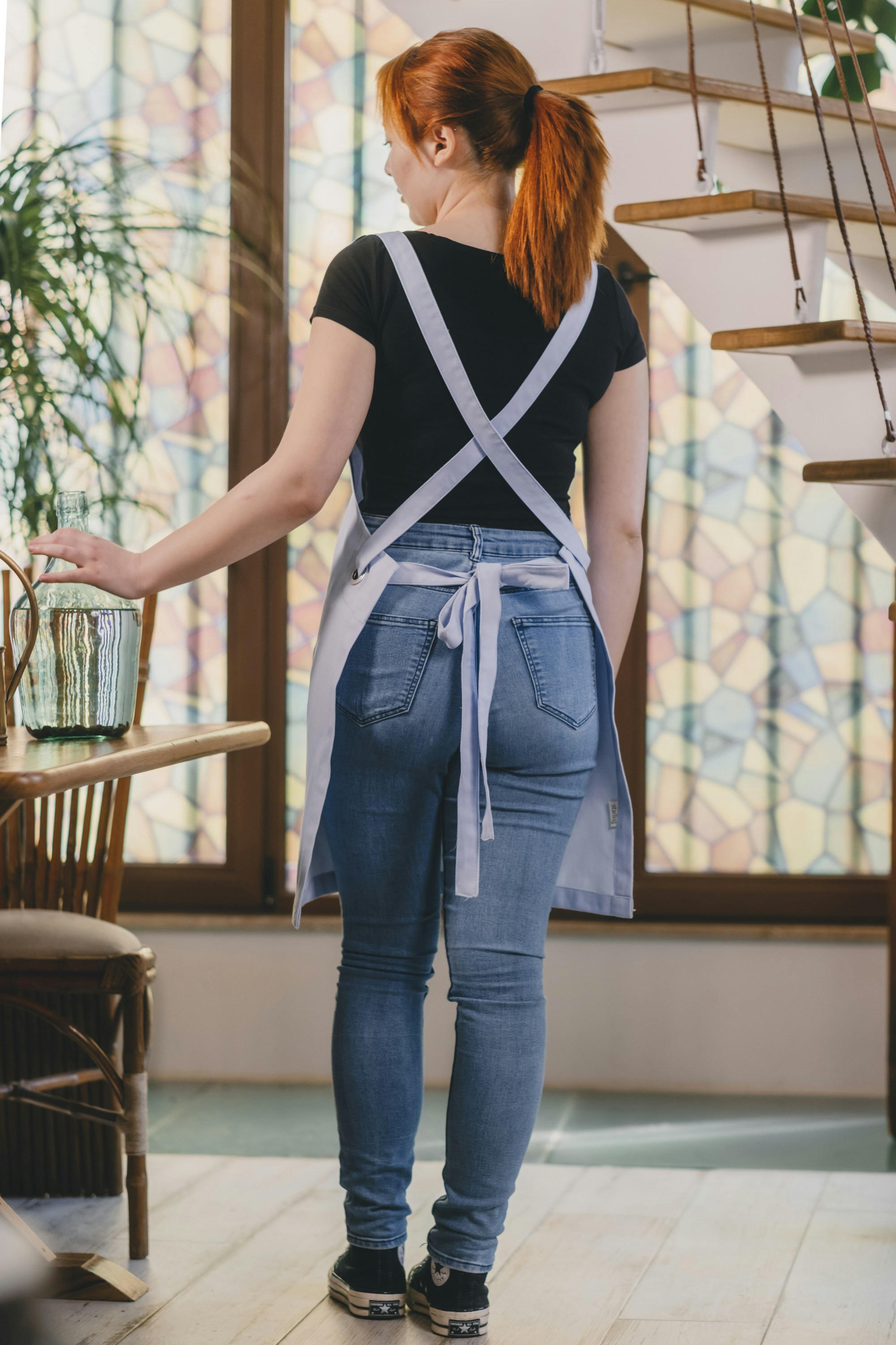 Back View of a Barista in a Cross-Back Apron Amid Colorful Stained-Glass Light