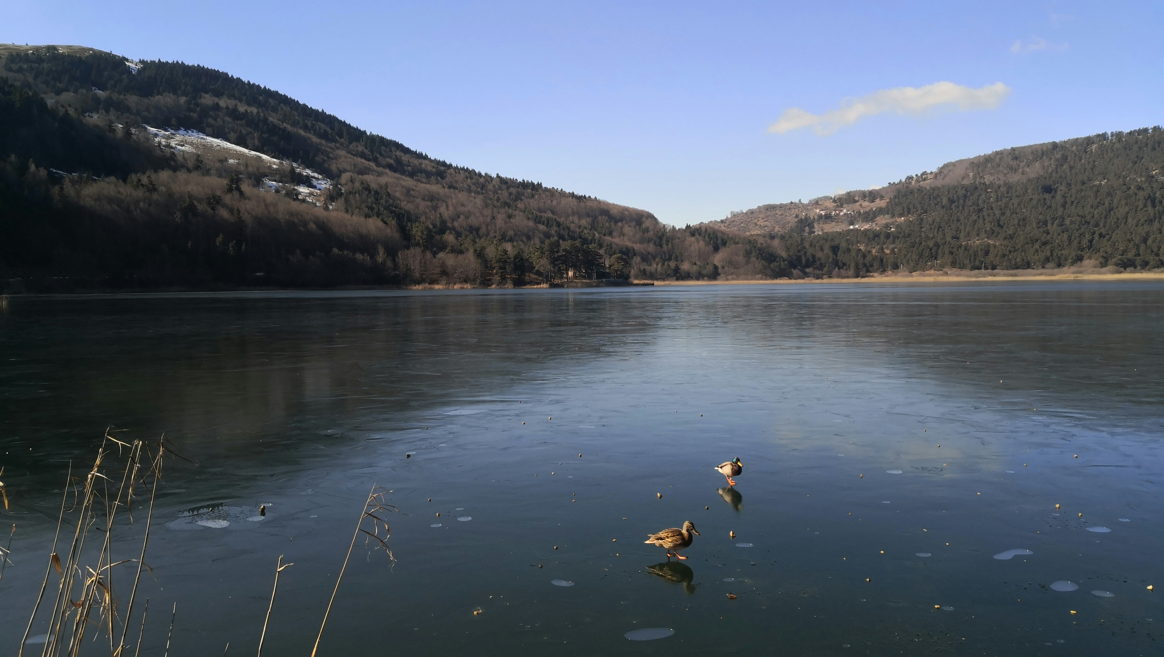 Calm lake surface reflecting surrounding snow-dusted mountains under a clear blue sky.