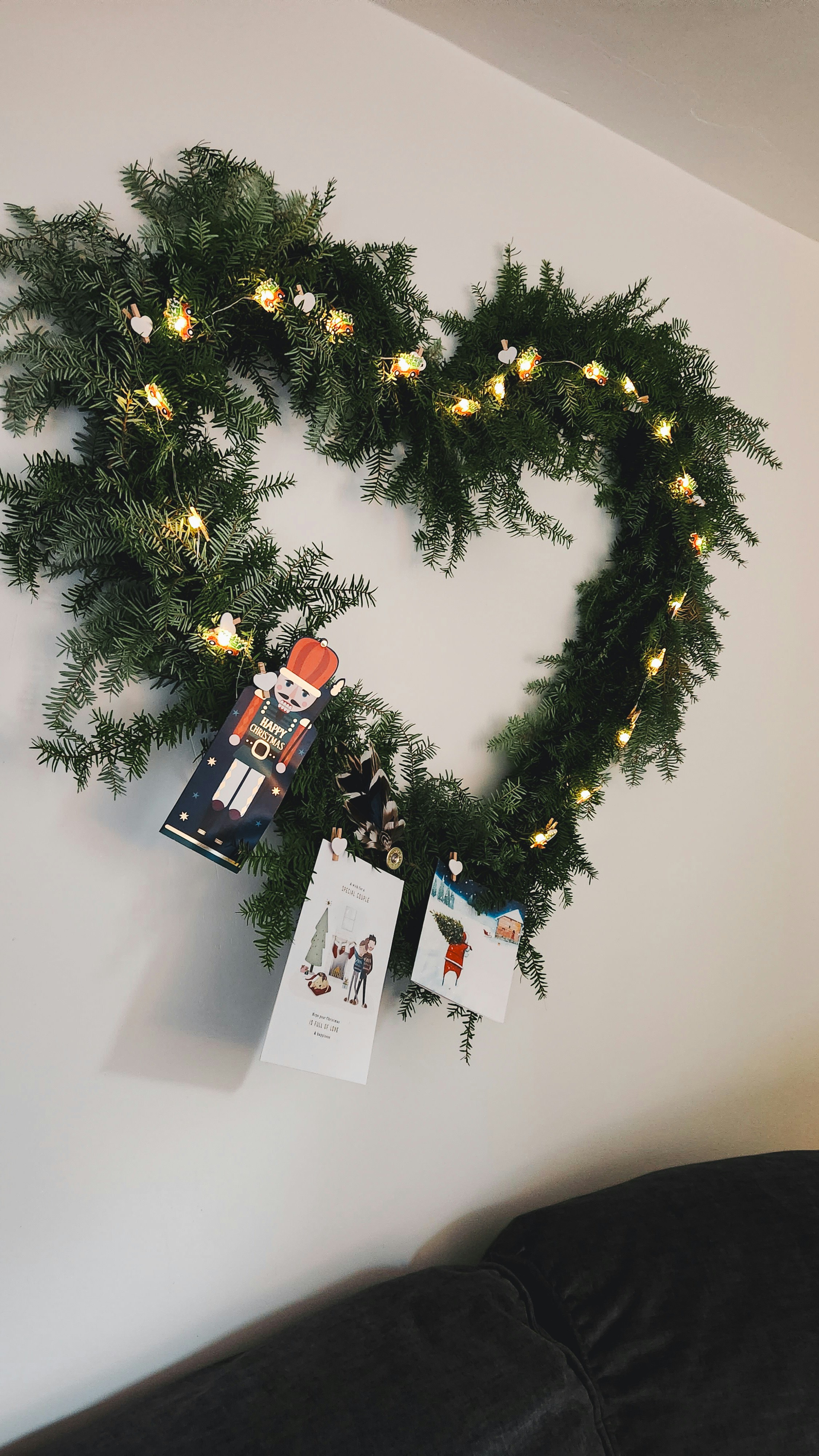 A heart-shaped wreath adorned with lights and holiday cards, creating a festive atmosphere on a wall. A nutcracker figurine adds a whimsical touch.