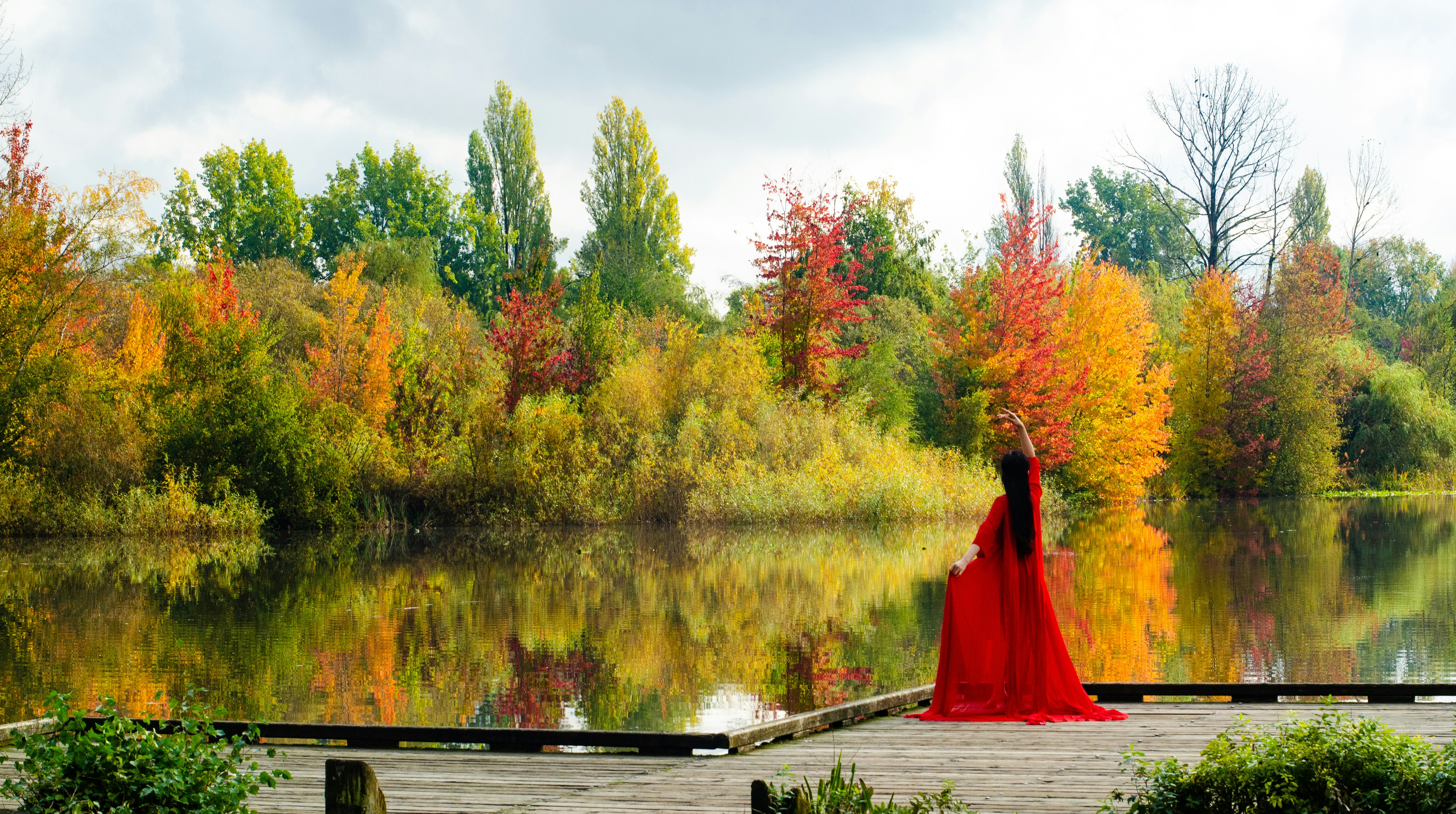 Red-dressed silhouette on a fall-hued lakeside dock