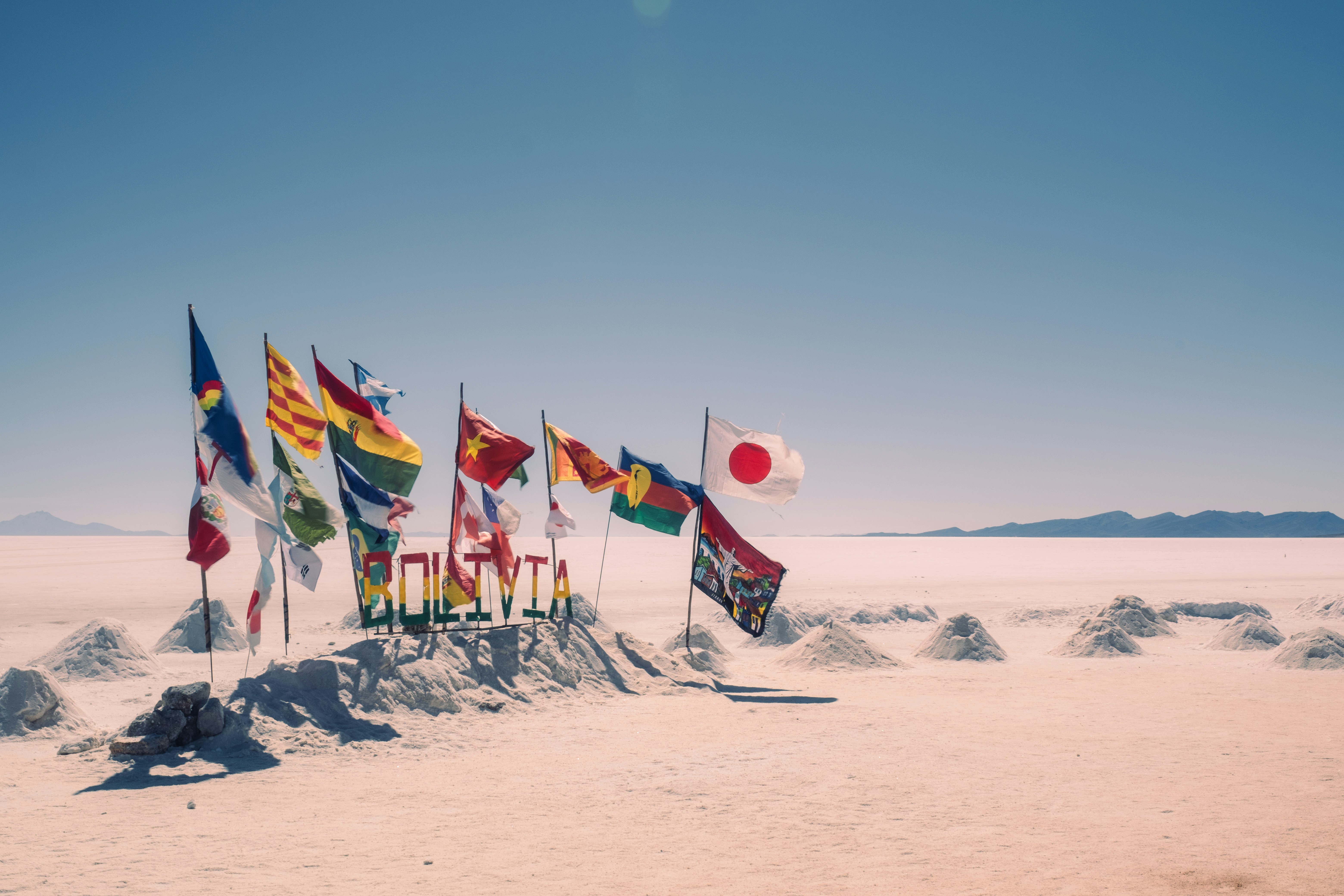 A vibrant display of international flags stands on the salt flats of Bolivia, symbolizing cultural unity against a vast, arid landscape.