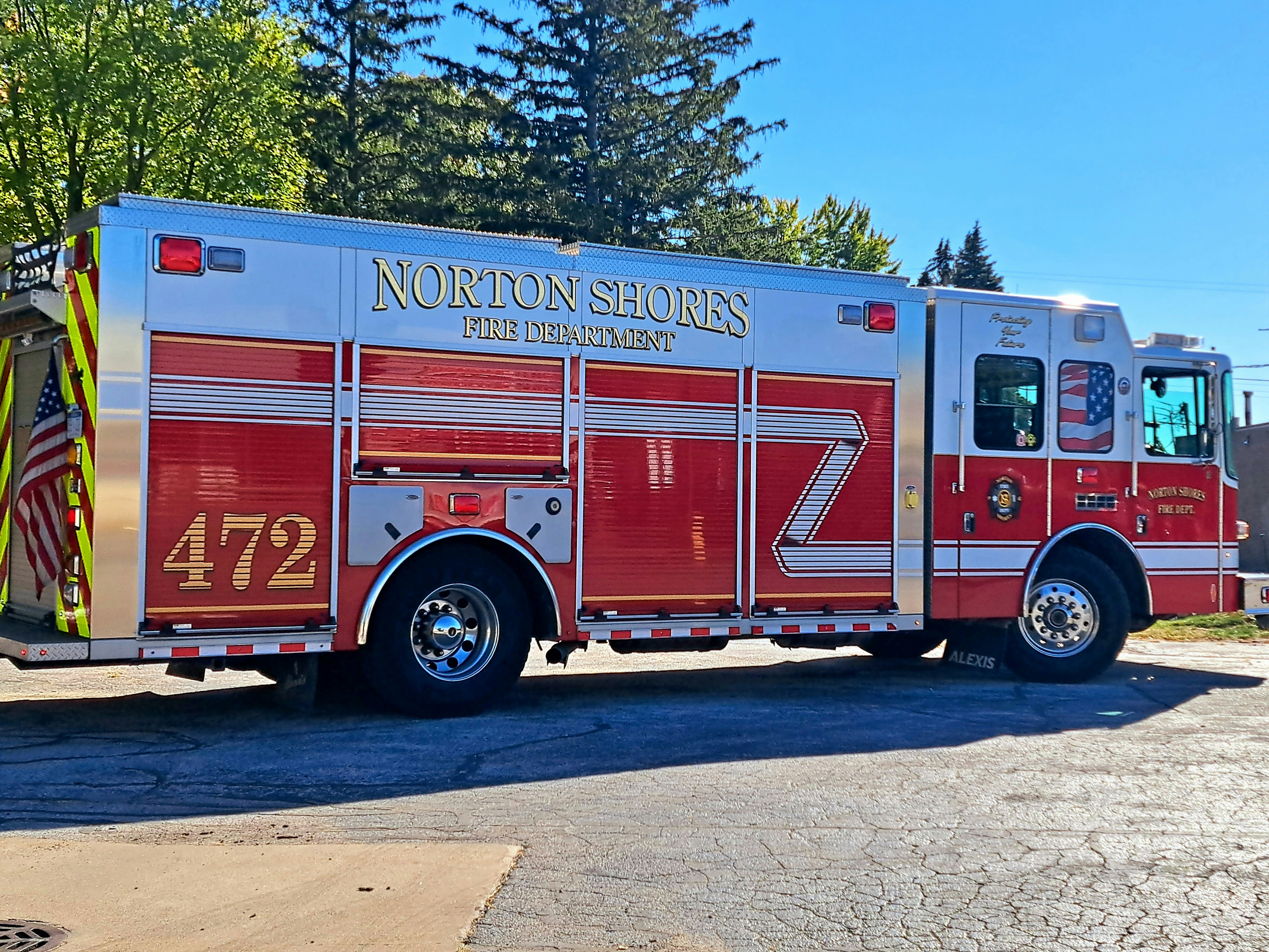 Red and white fire truck parked outdoors with clear blue sky and trees in the background.