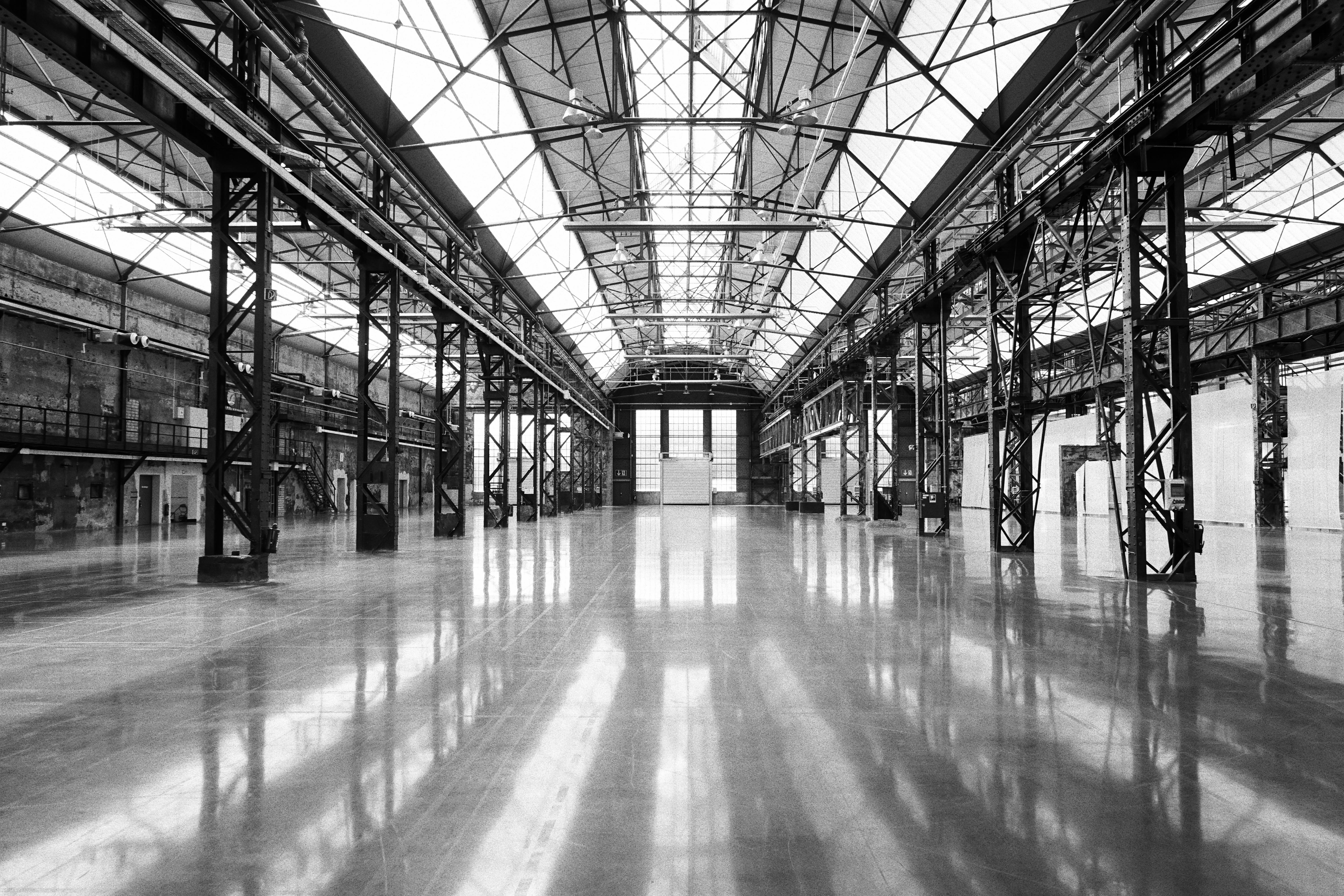 Black and white industrial interior with steel beams and reflective floors beneath a vast glass ceiling.