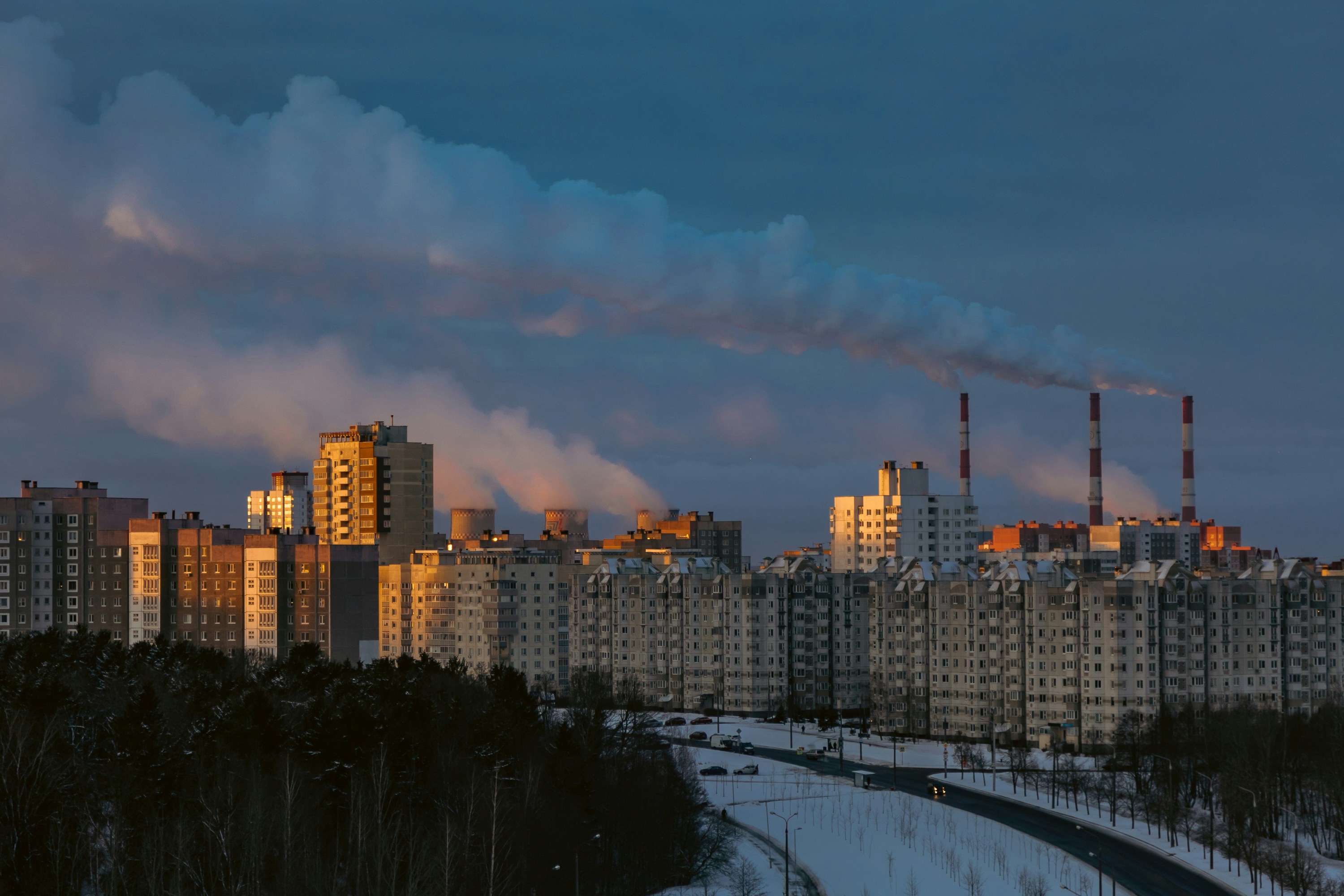 City skyline with smoke rising from chimneys under a dusky sky.
