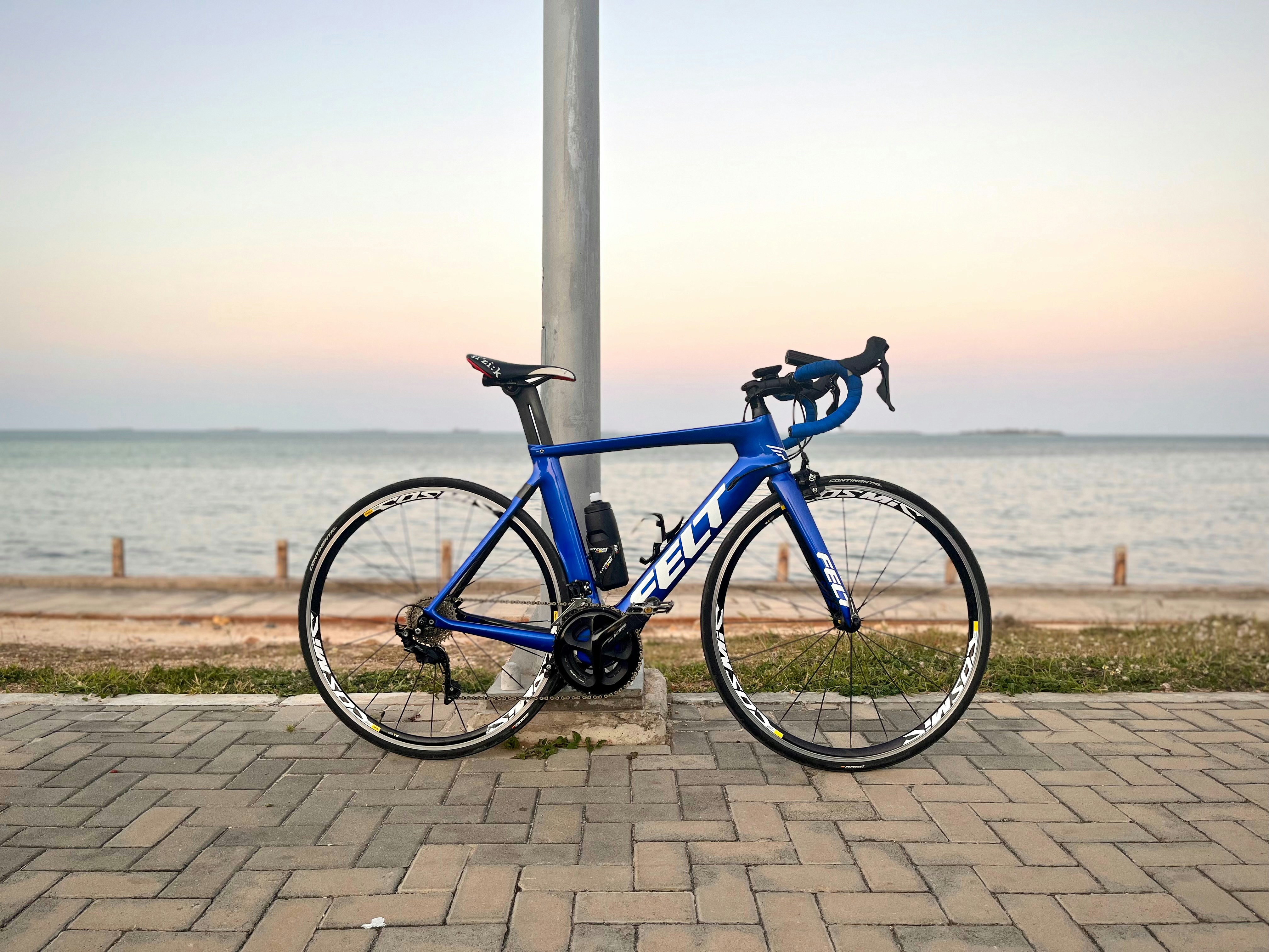 A blue bike is parked next to a pole photo – Free Road bike Image on ...