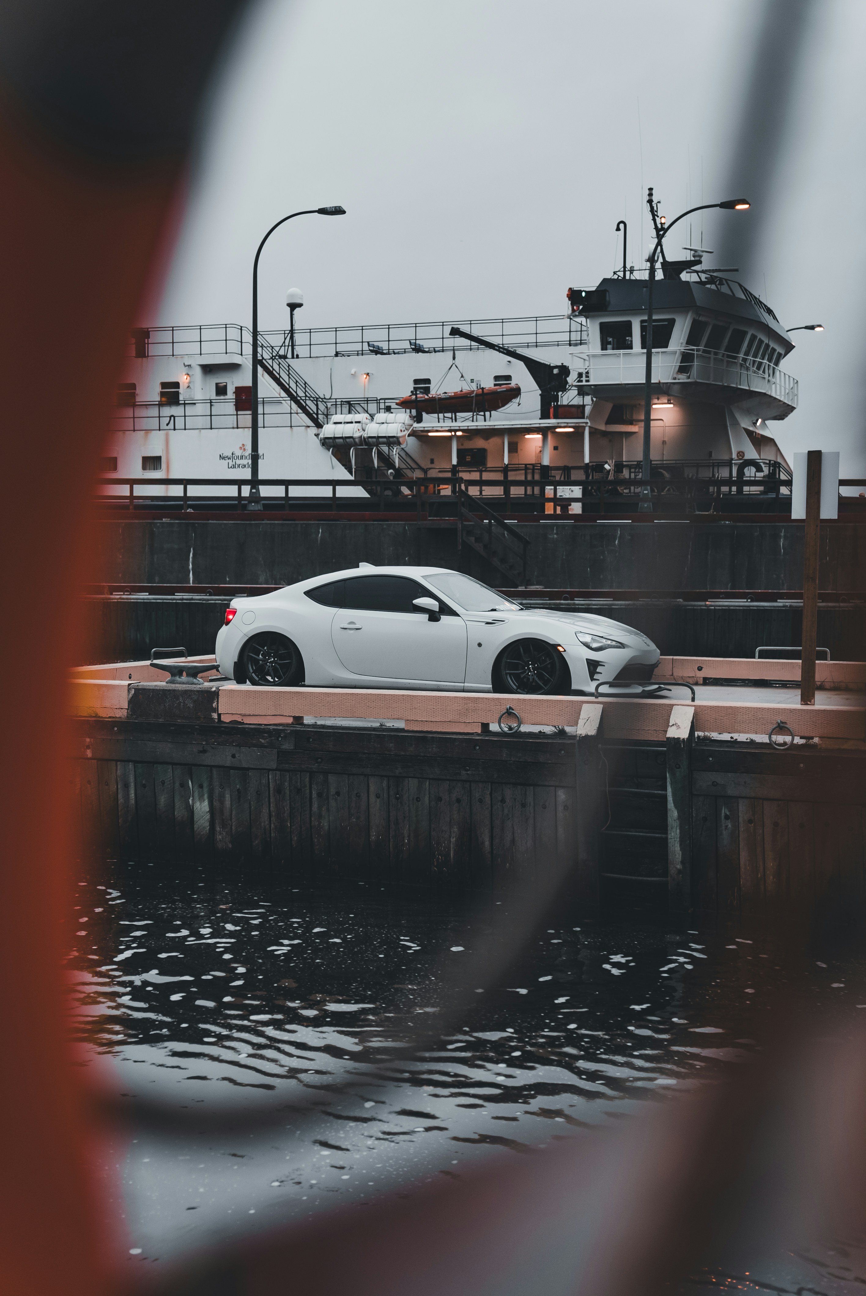 White sports coupe on a dock framed by industrial harbor rails
