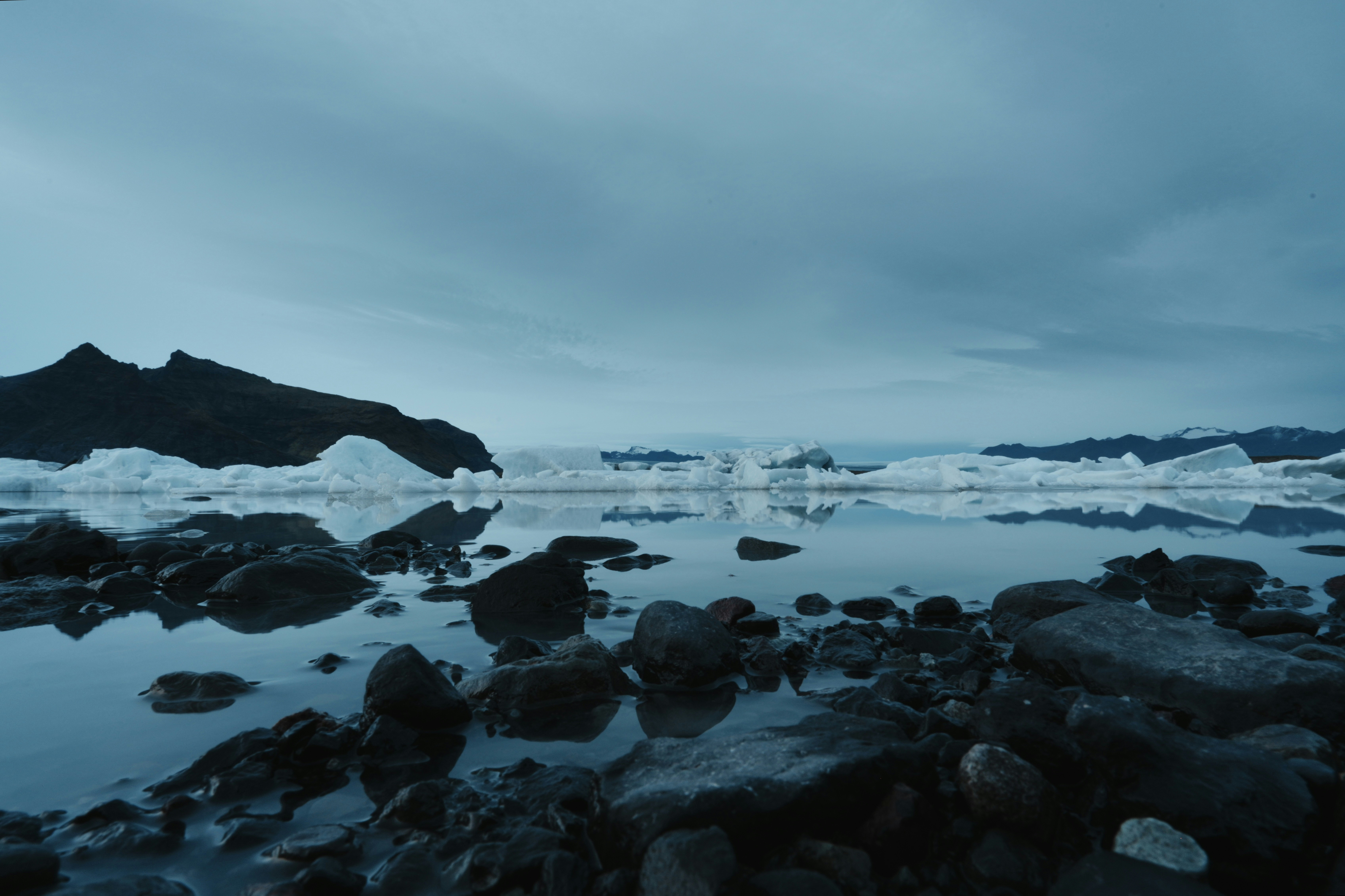 A body of water surrounded by rocks under a cloudy sky photo – Free ...