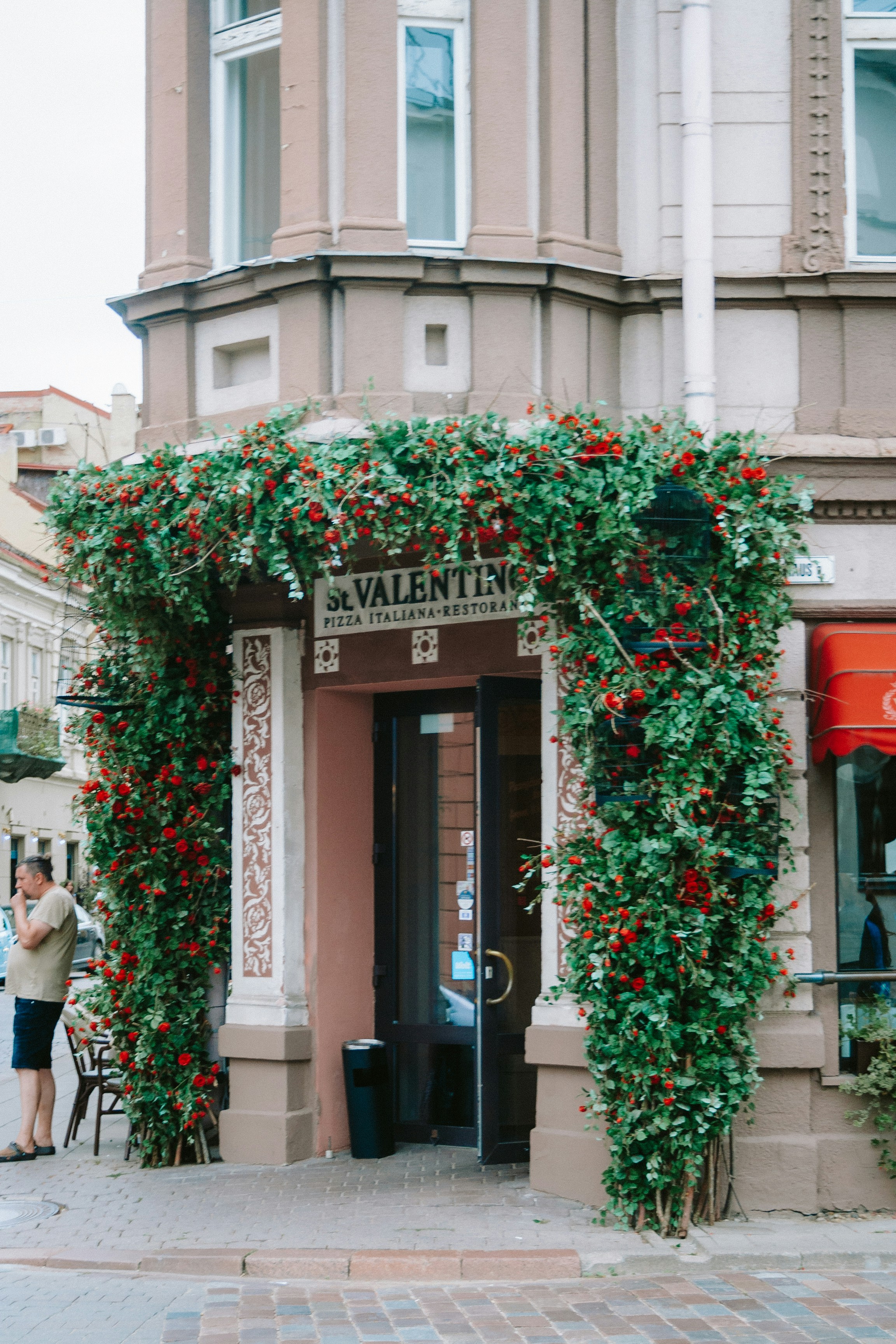 Ivy-Archway Café: Entrance Framed by Crimson Blooms on a Cobblestone Street