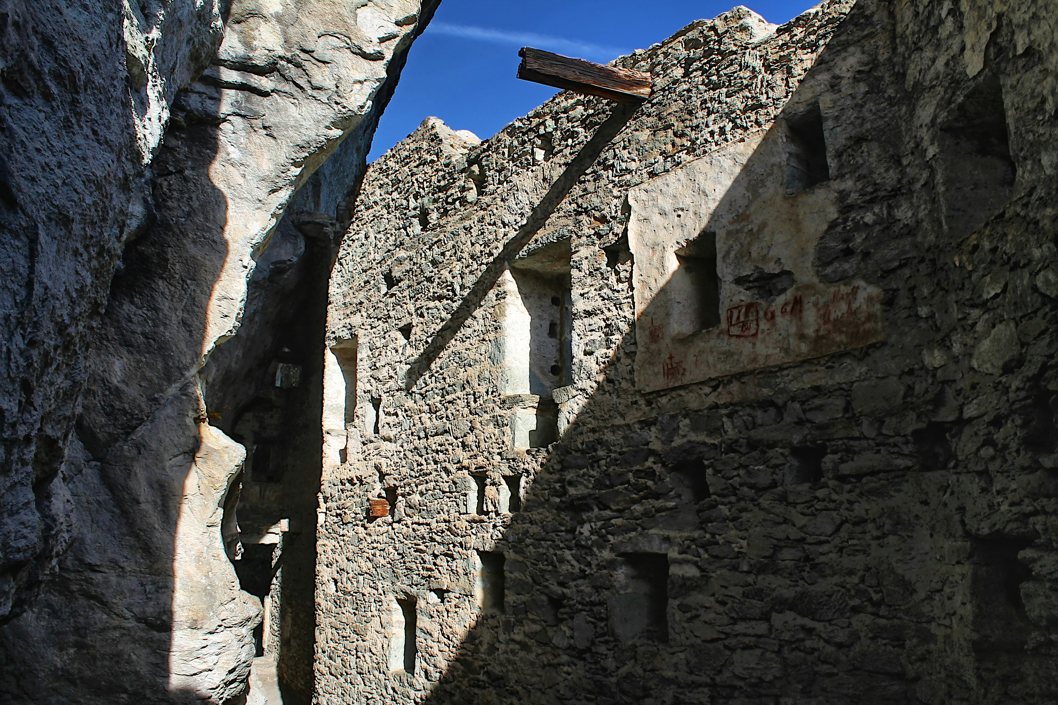 Ruins of an ancient structure nestled between towering rock formations, illuminated by natural light.