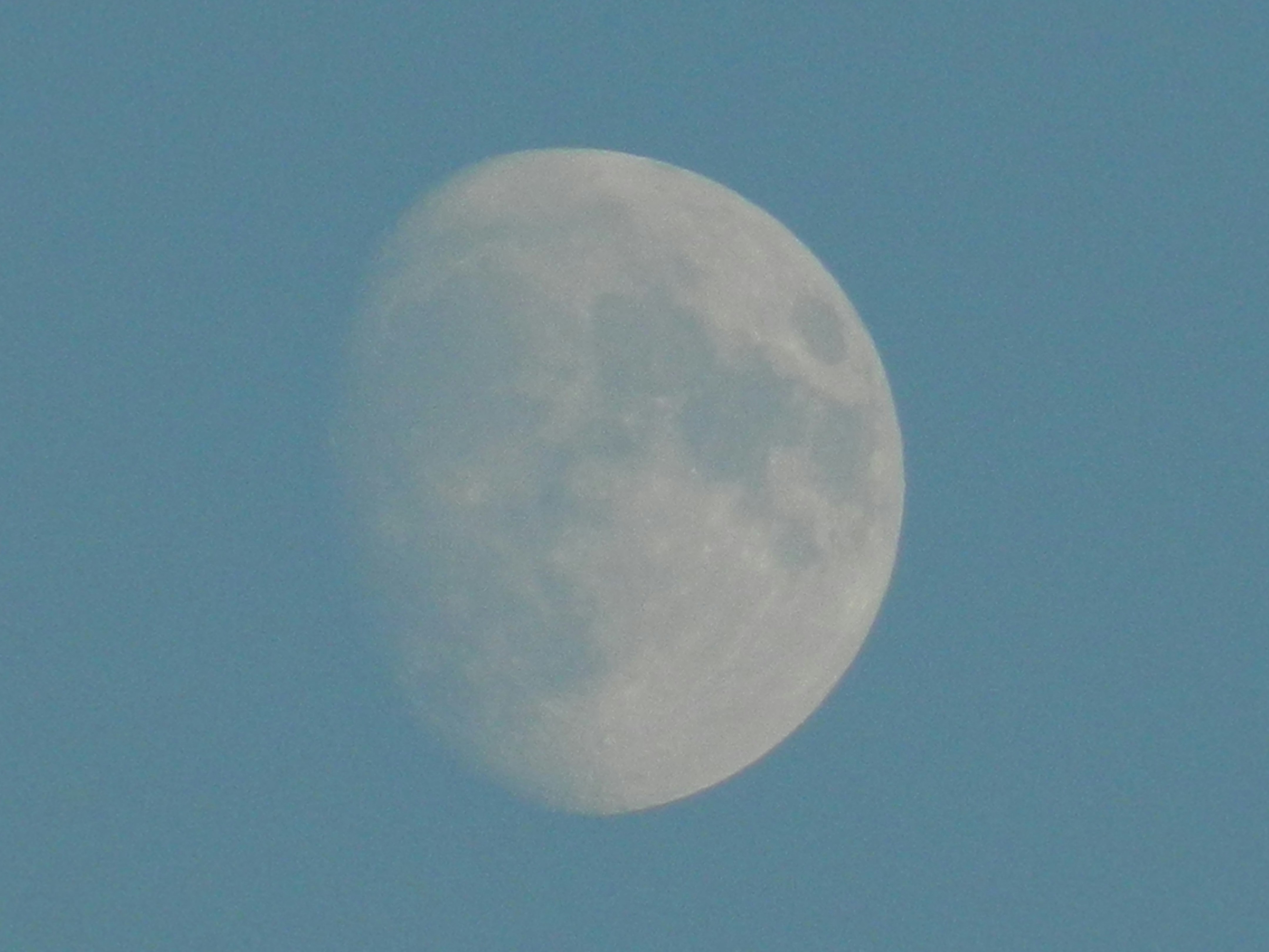 Gibbous Moon against a clear blue sky, revealing visible lunar maria and crater details.