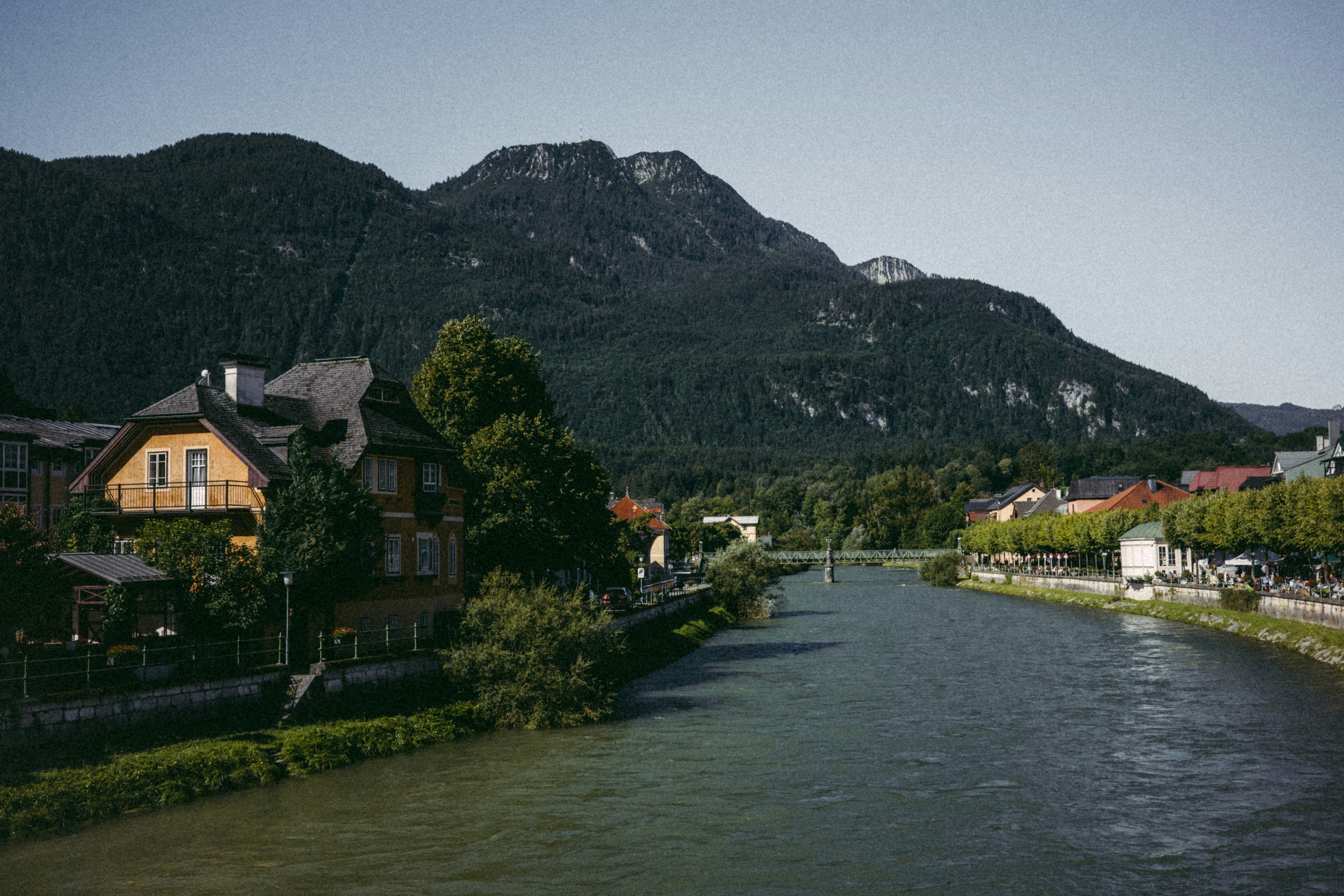 Peaceful river flowing through a quaint Austrian town with majestic mountains in the background.