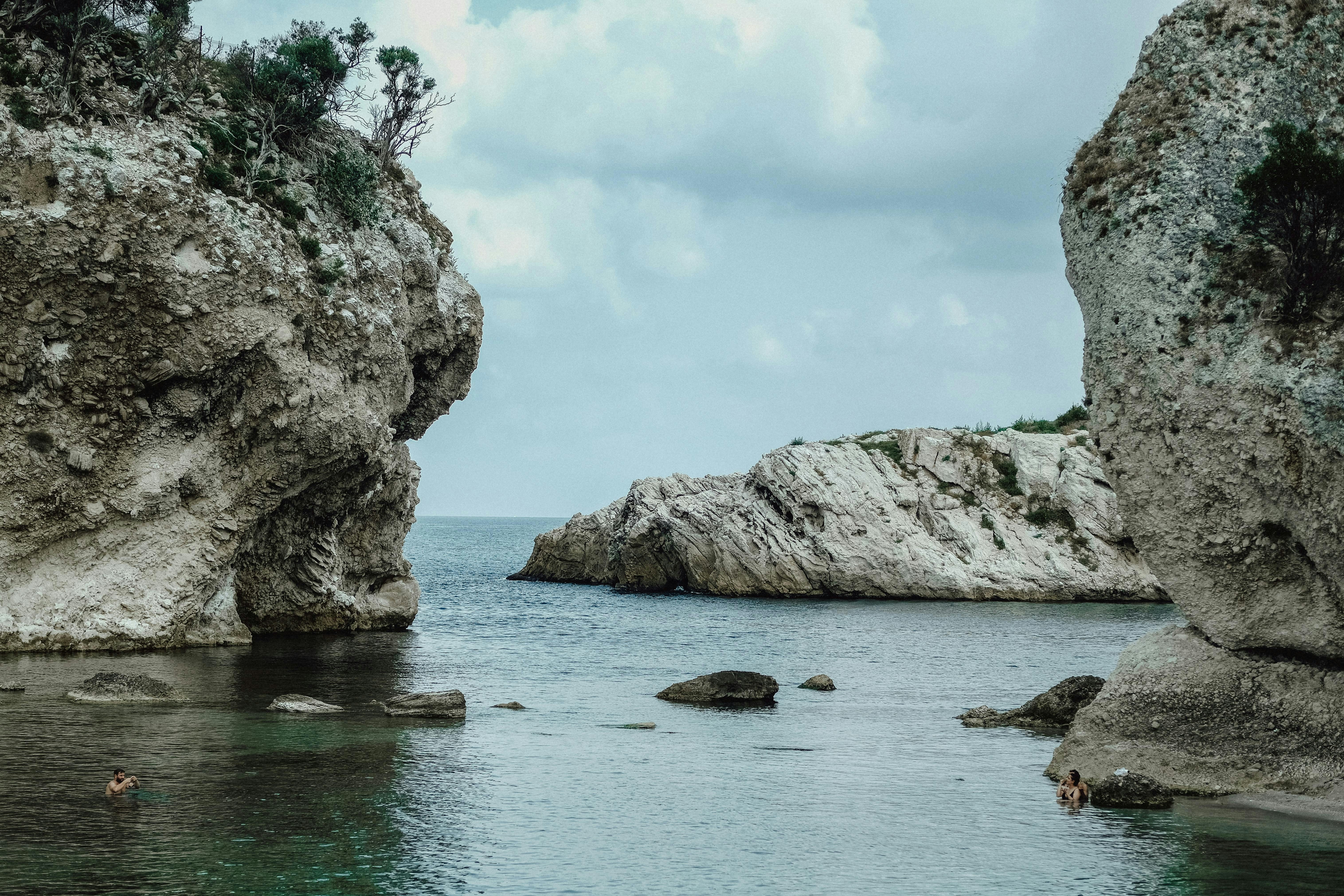 A body of water surrounded by large rocks photo – Free Rock Image on ...
