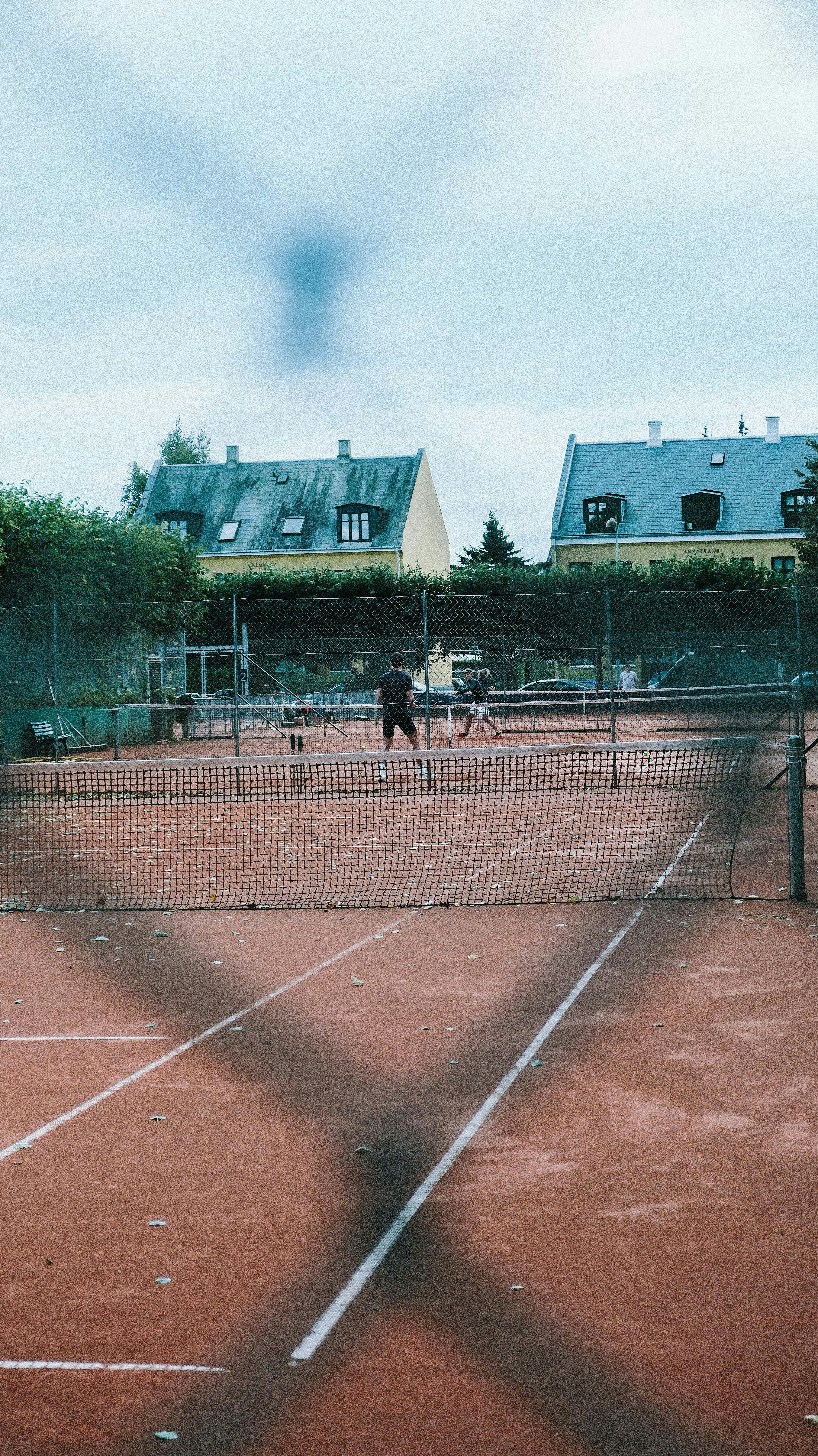 Distant Rally on a Red Clay Court: Nets, Neighbors, and Afternoon Light
