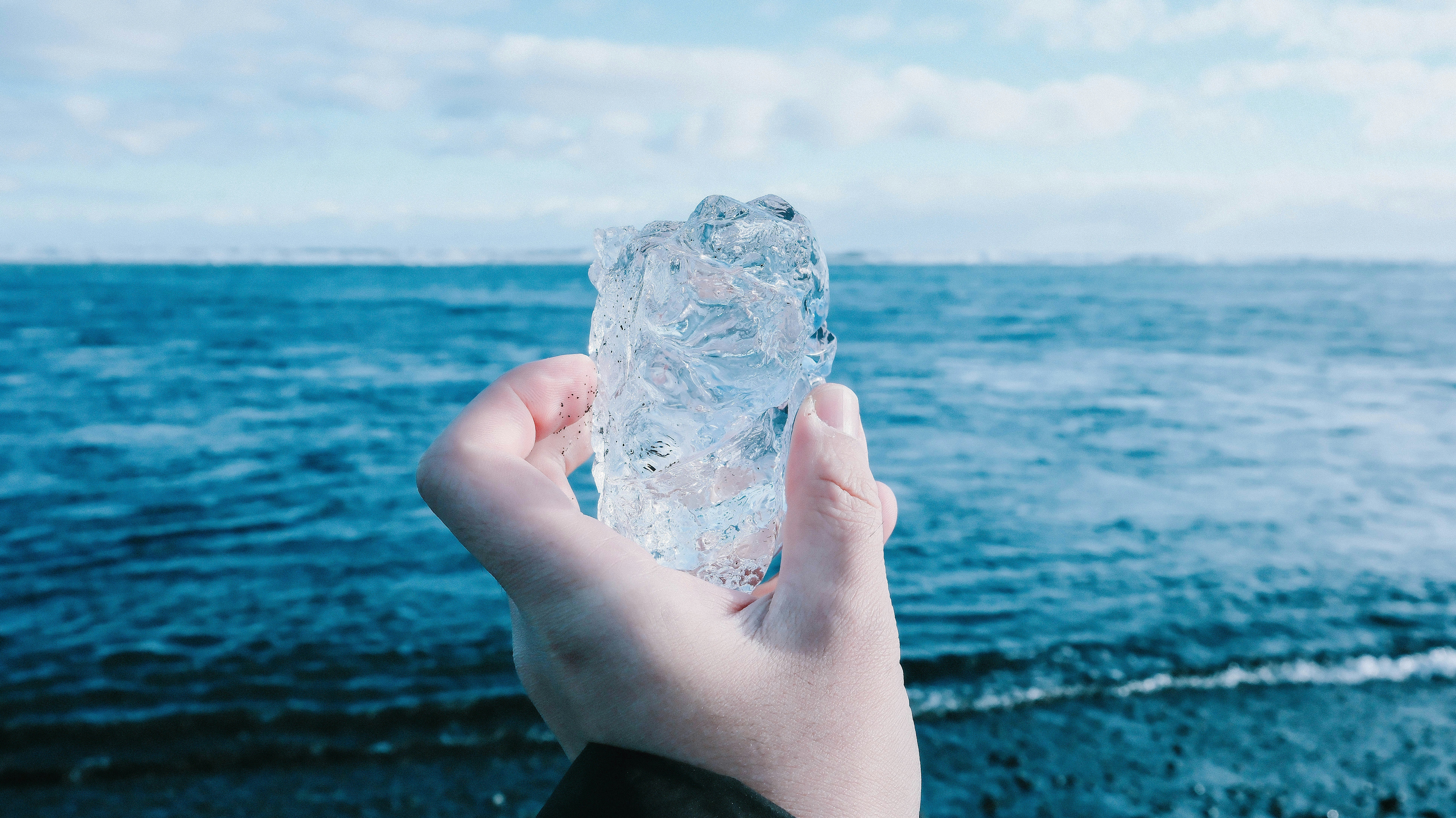 A hand holding a piece of ice over a body of water photo – Free Beach ...