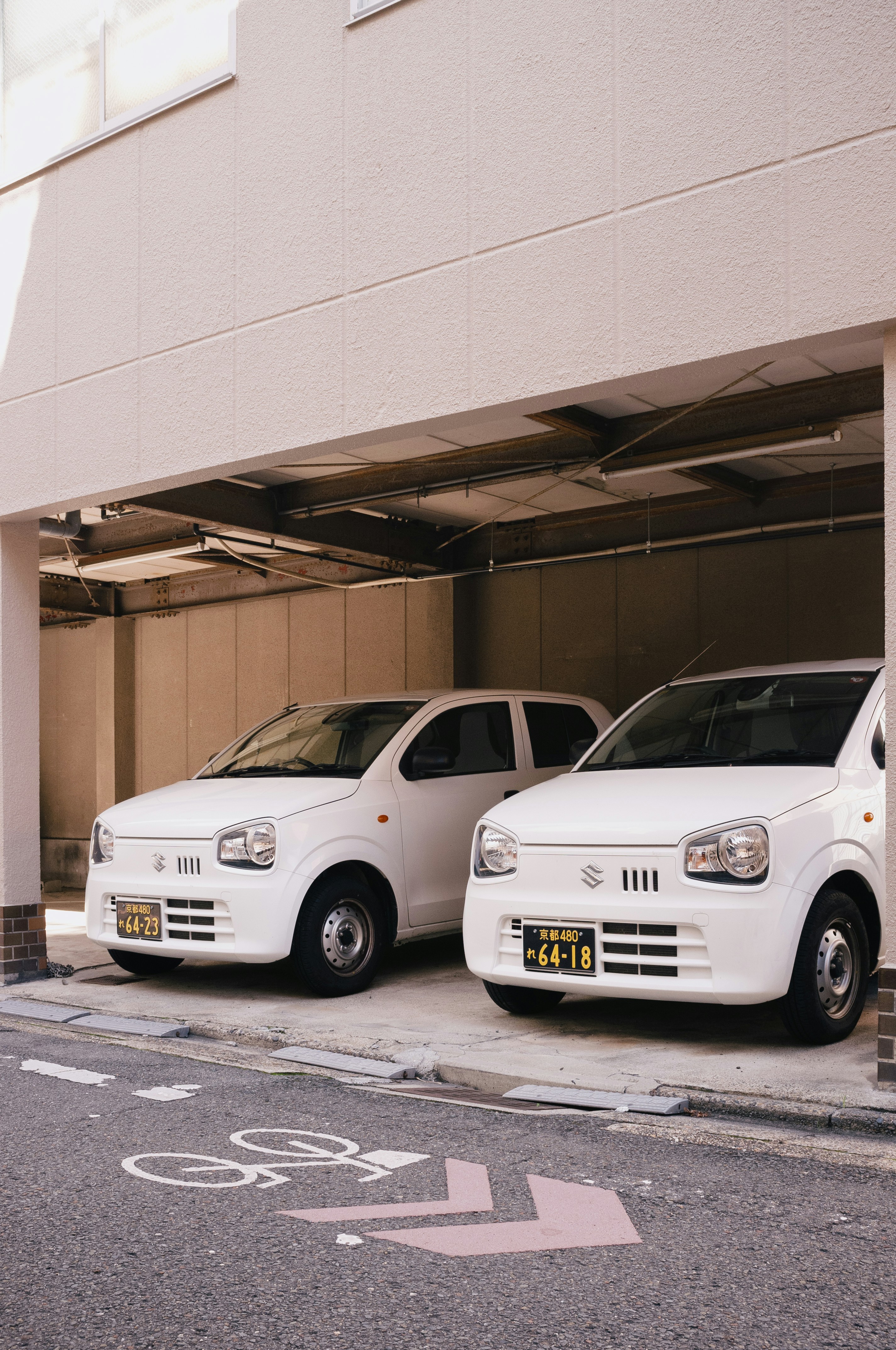 White compact cars under a shaded overhang in an urban parking bay