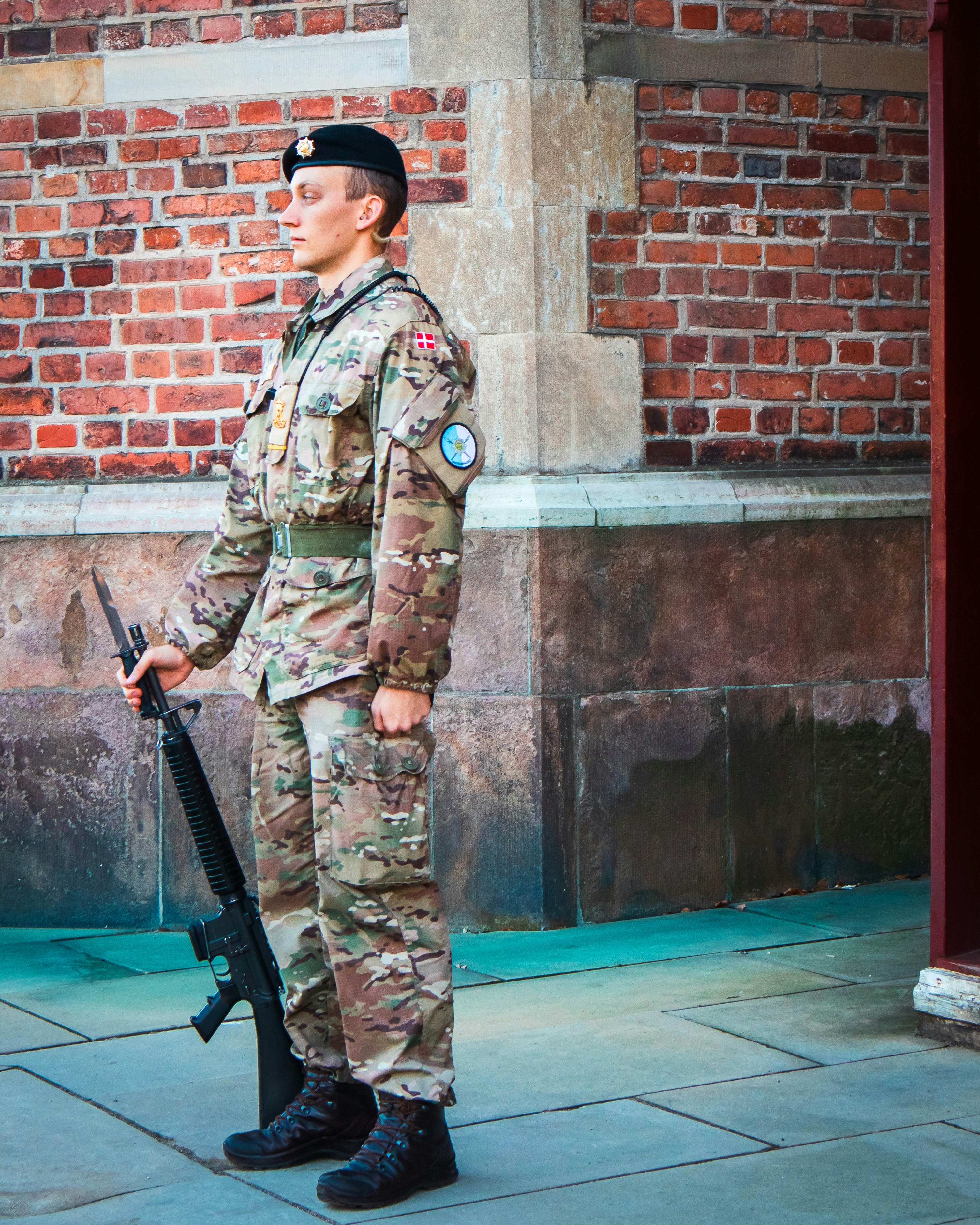 Still Guard Before the Brick: A Camouflage Soldier Pauses with Rifle
