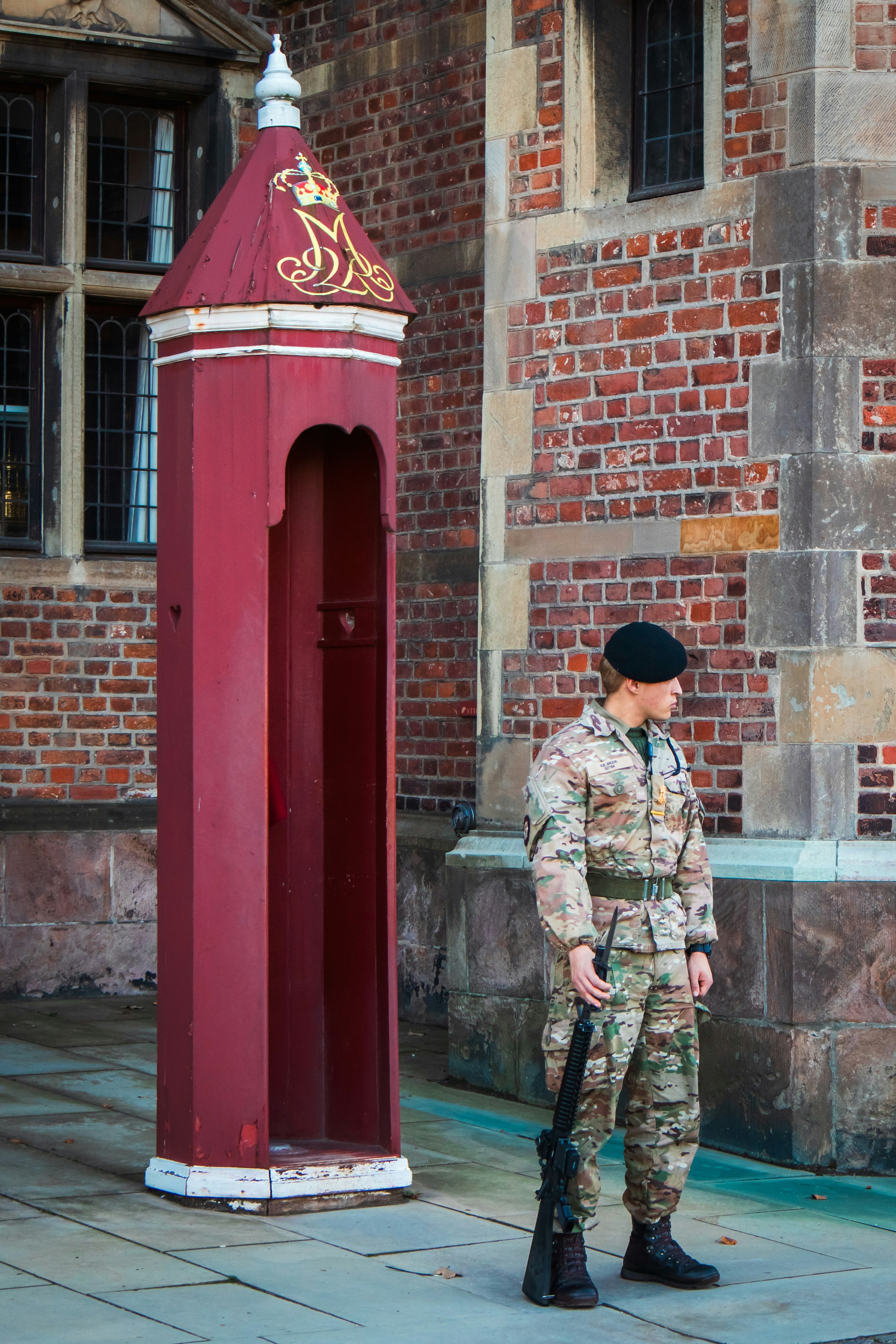 Red Booth, Quiet Sentinel: A Soldier Stands by a Historic Brick Facade