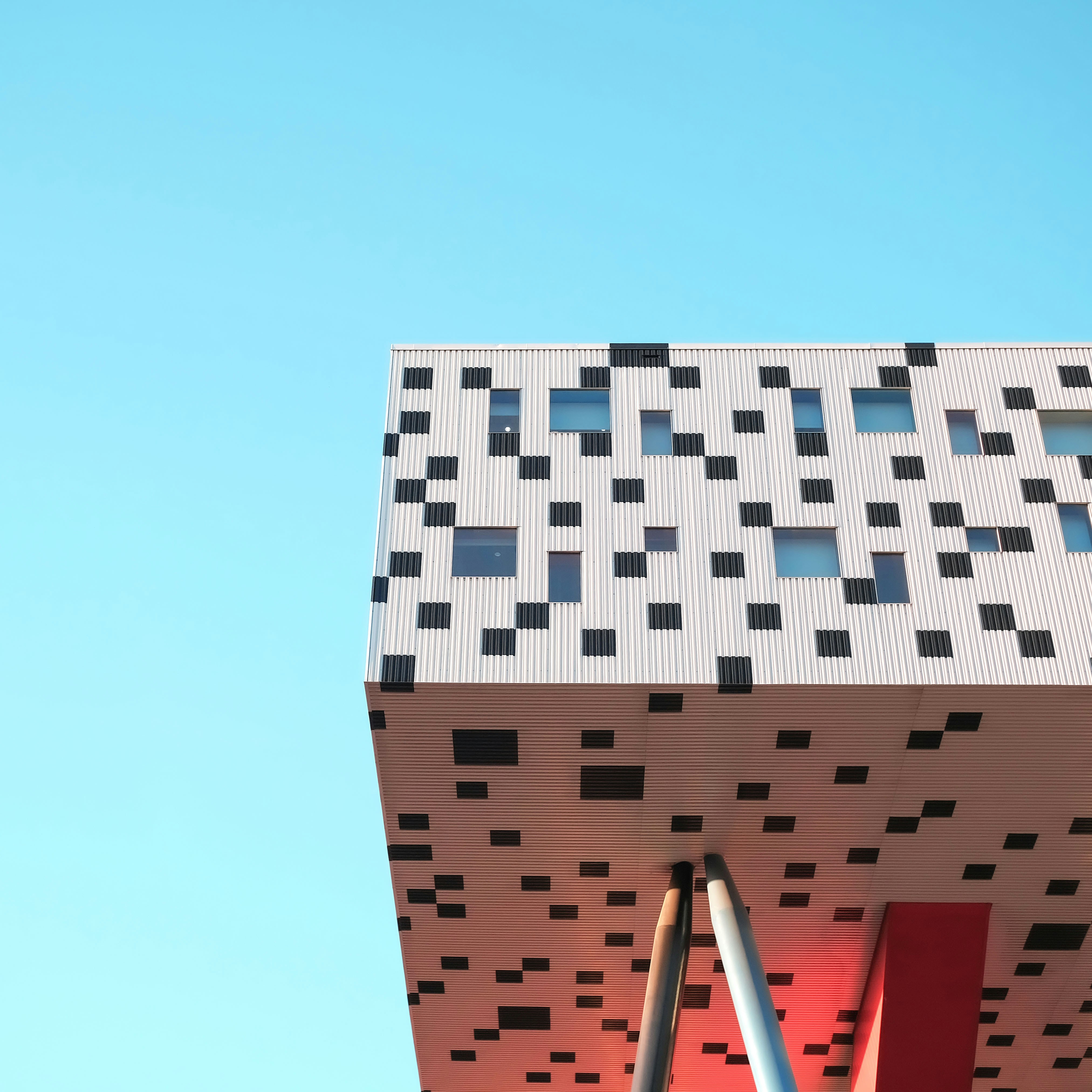 Pixel Grid Cantilever: Facade of Shadowed Squares Against a Clear Blue Sky