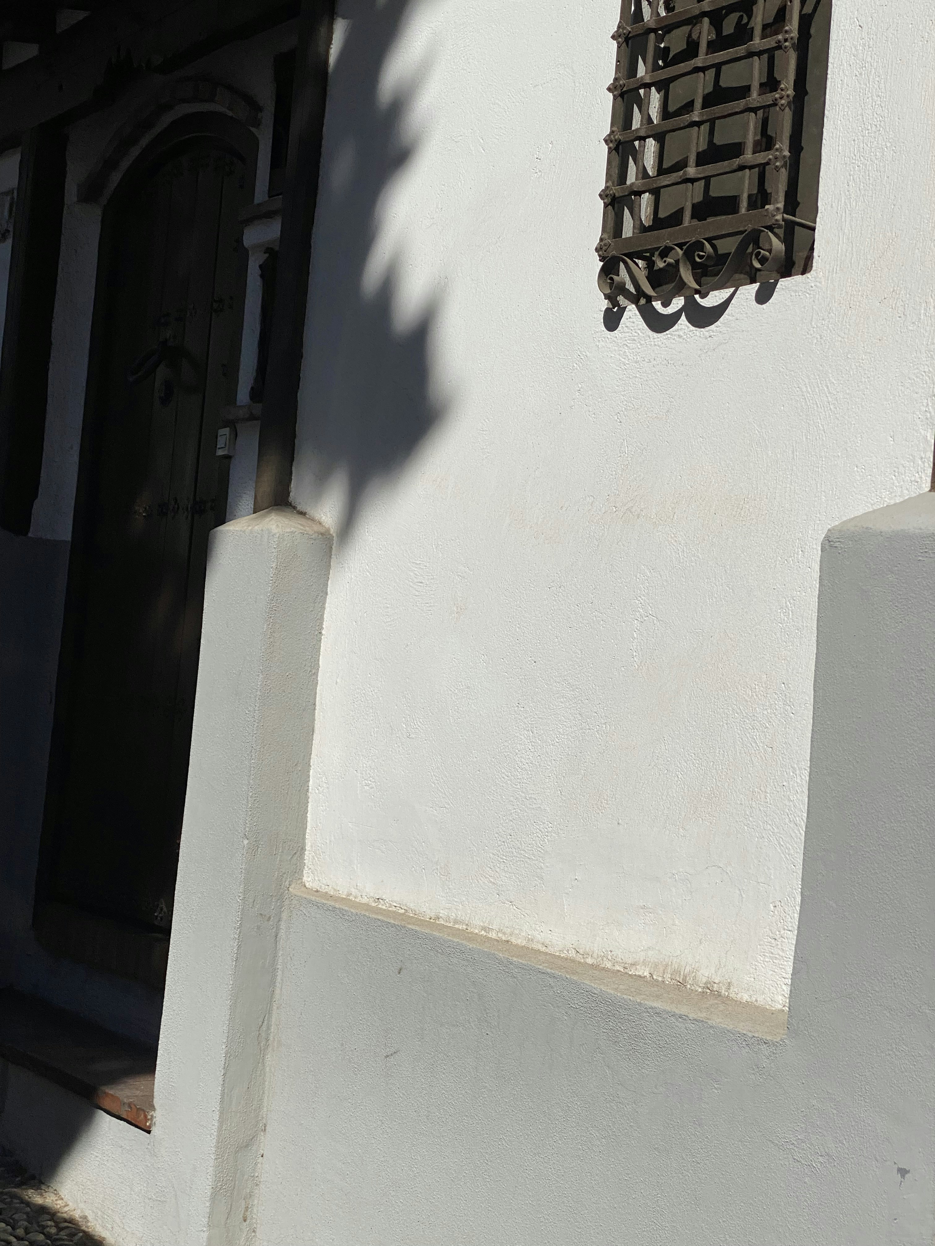 Quiet Daylight on a White Facade: Iron Grille and Shadowed Doorway
