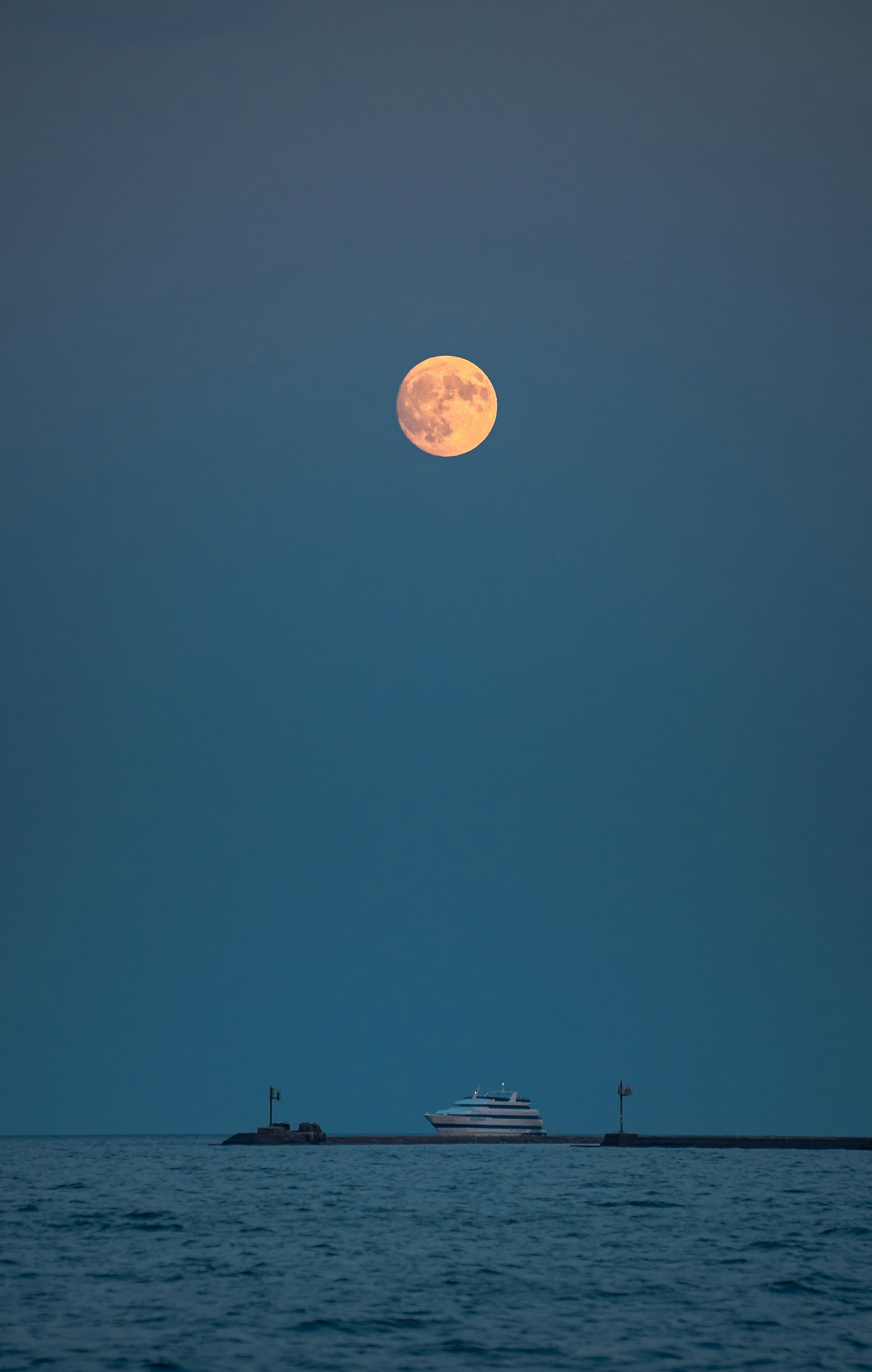 A full moon rising over the ocean with a cruise ship in the distance ...