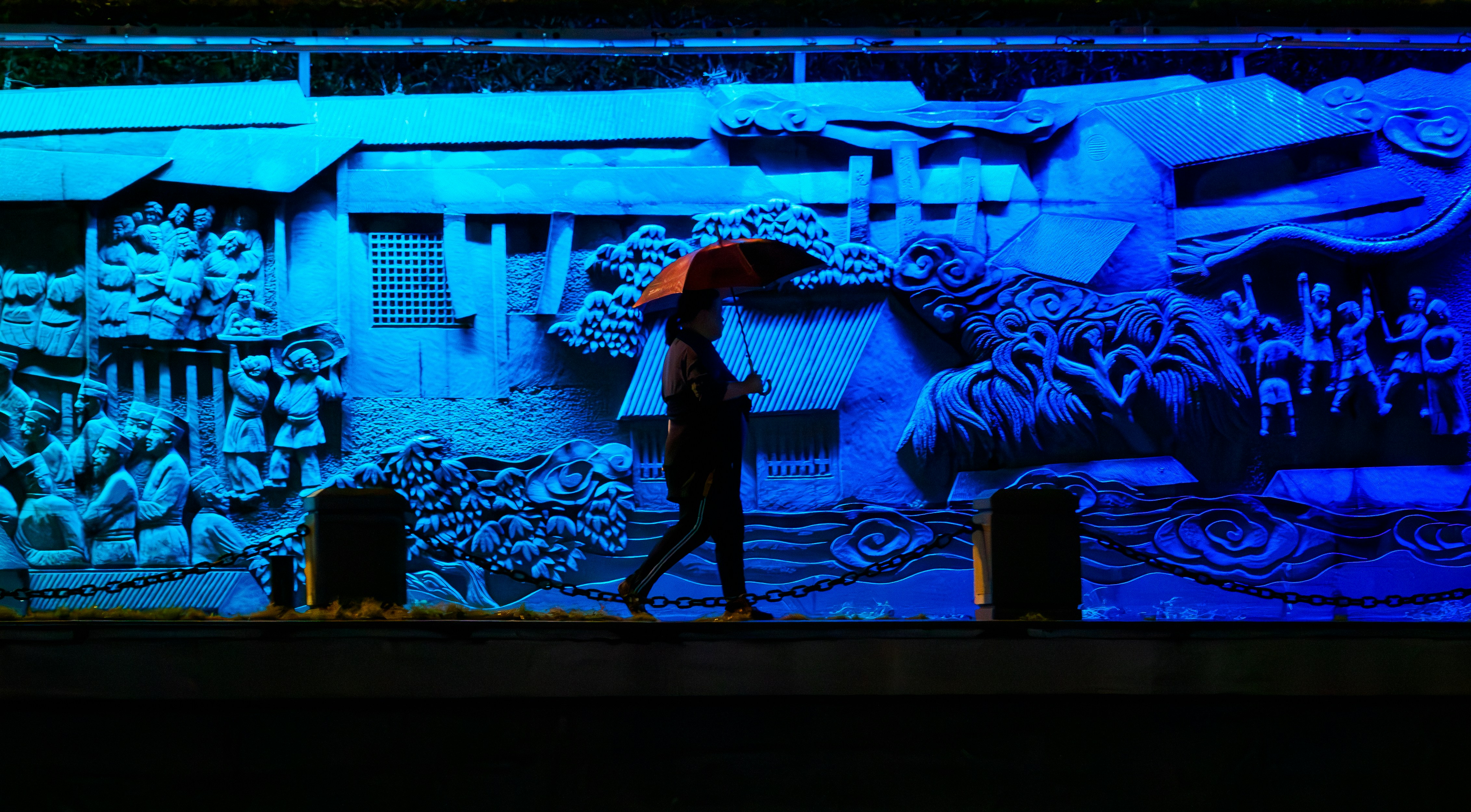 A person holding an umbrella walking in front of a wall