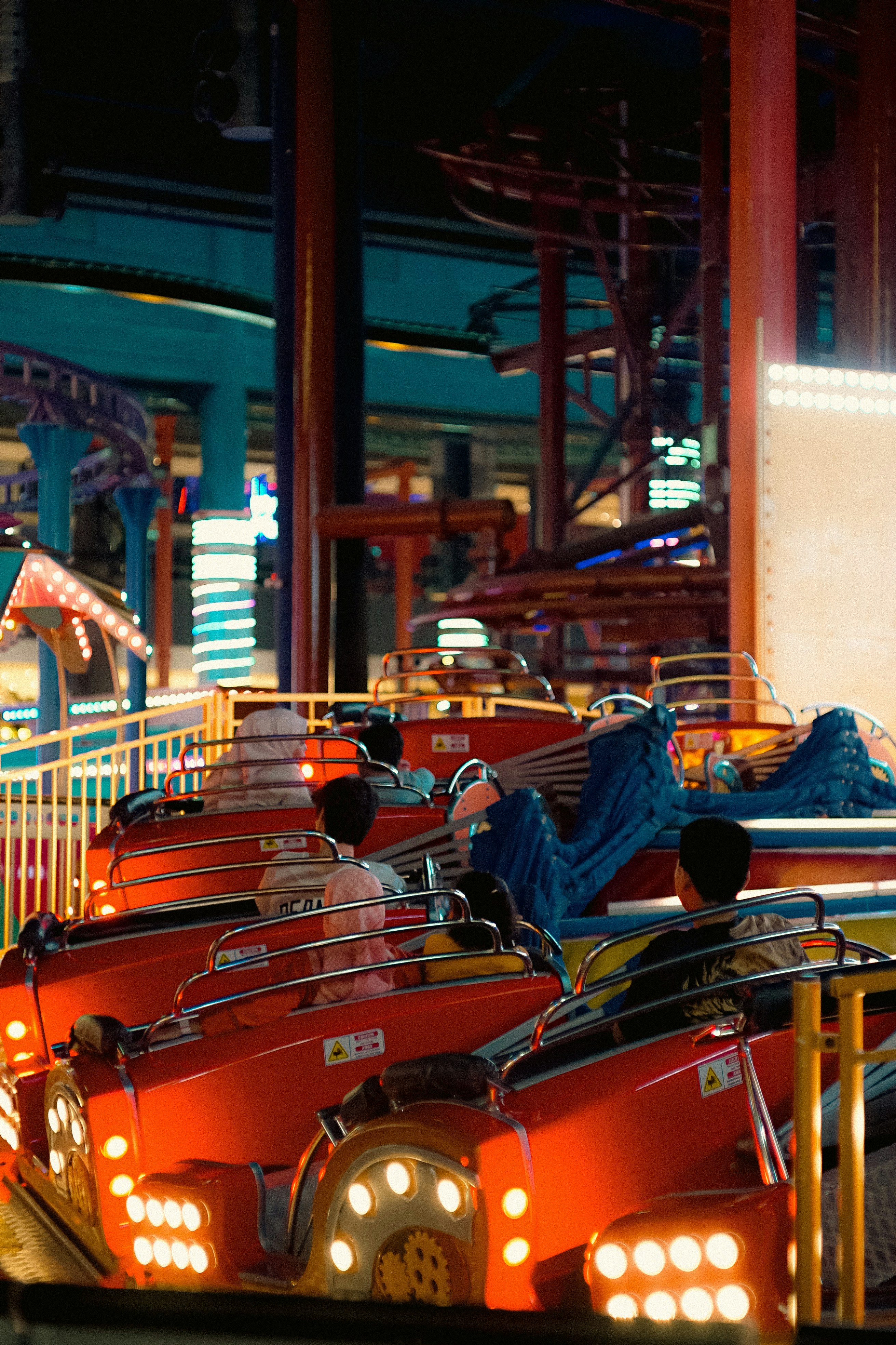 Midnight Neon: Orange Coaster Cars Glide Through a Turquoise-Embellished Indoor Night