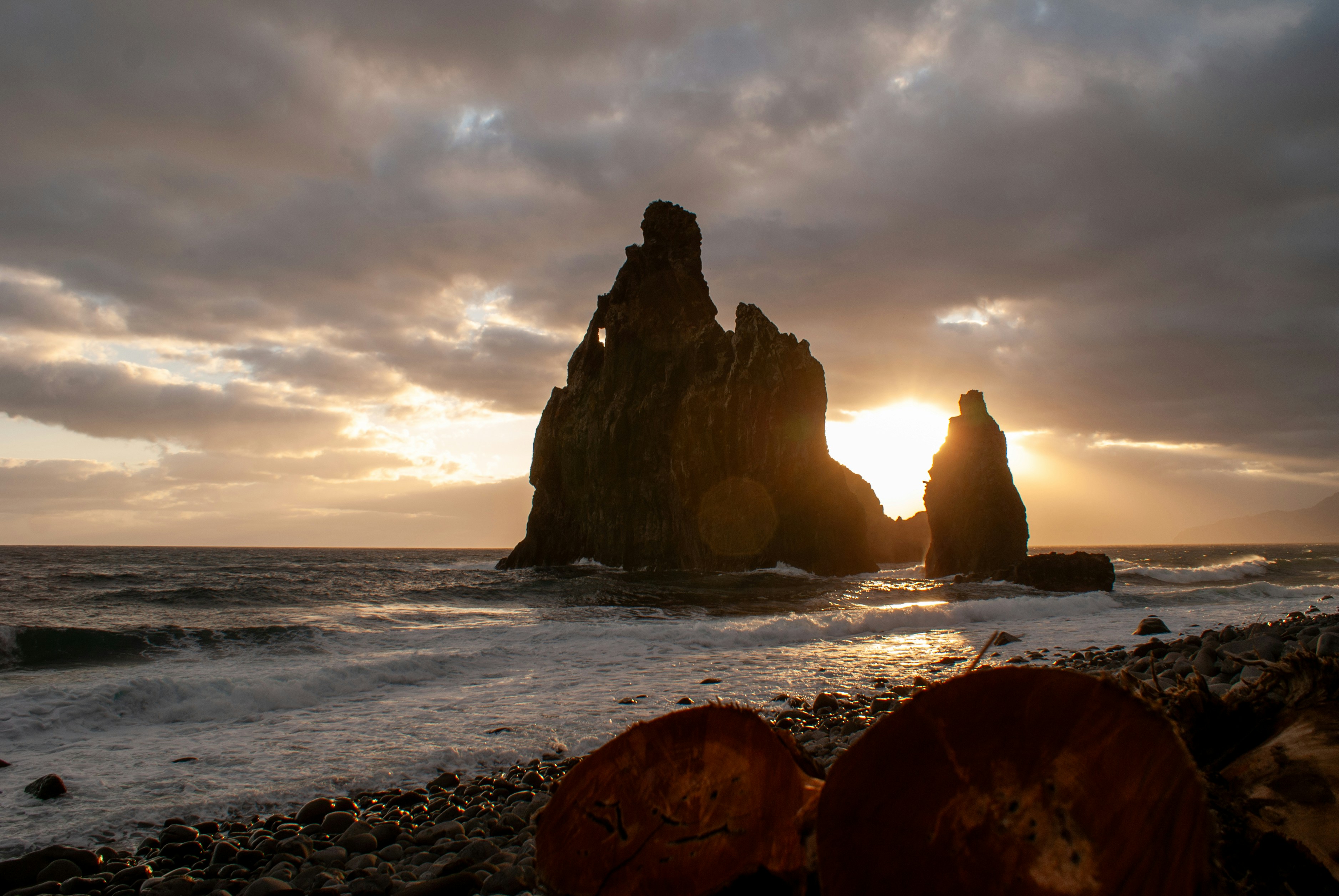Jagged sea stacks silhouetted against a sunset, with warm light reflecting on ocean waves and rocky shoreline.