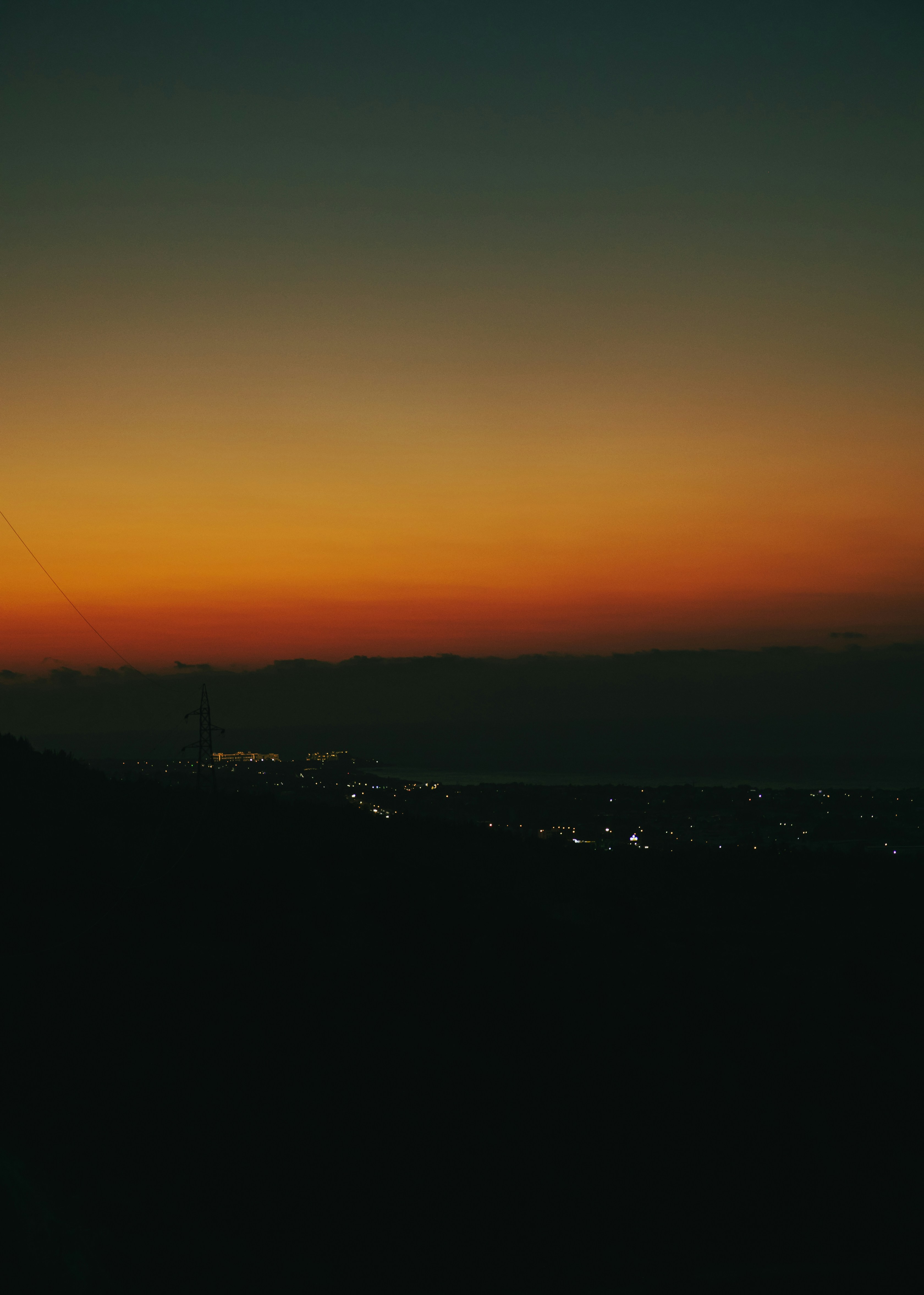 Vibrant sunset hues blend seamlessly into twilight, illuminating distant city lights along the coastline.