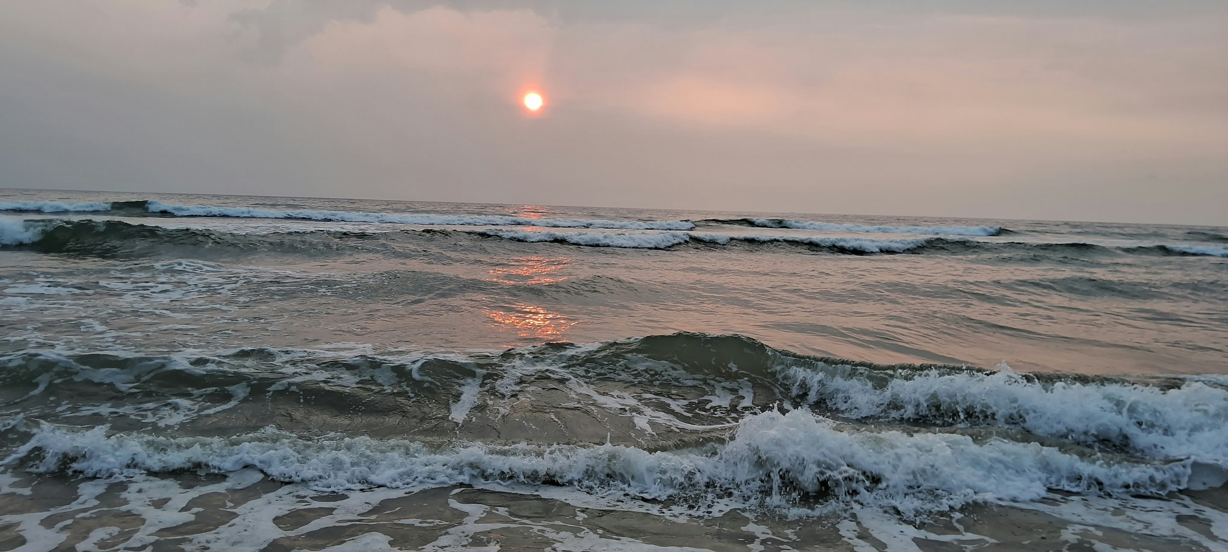 Sunset casting a warm glow over gentle ocean waves, creating a serene beach atmosphere.