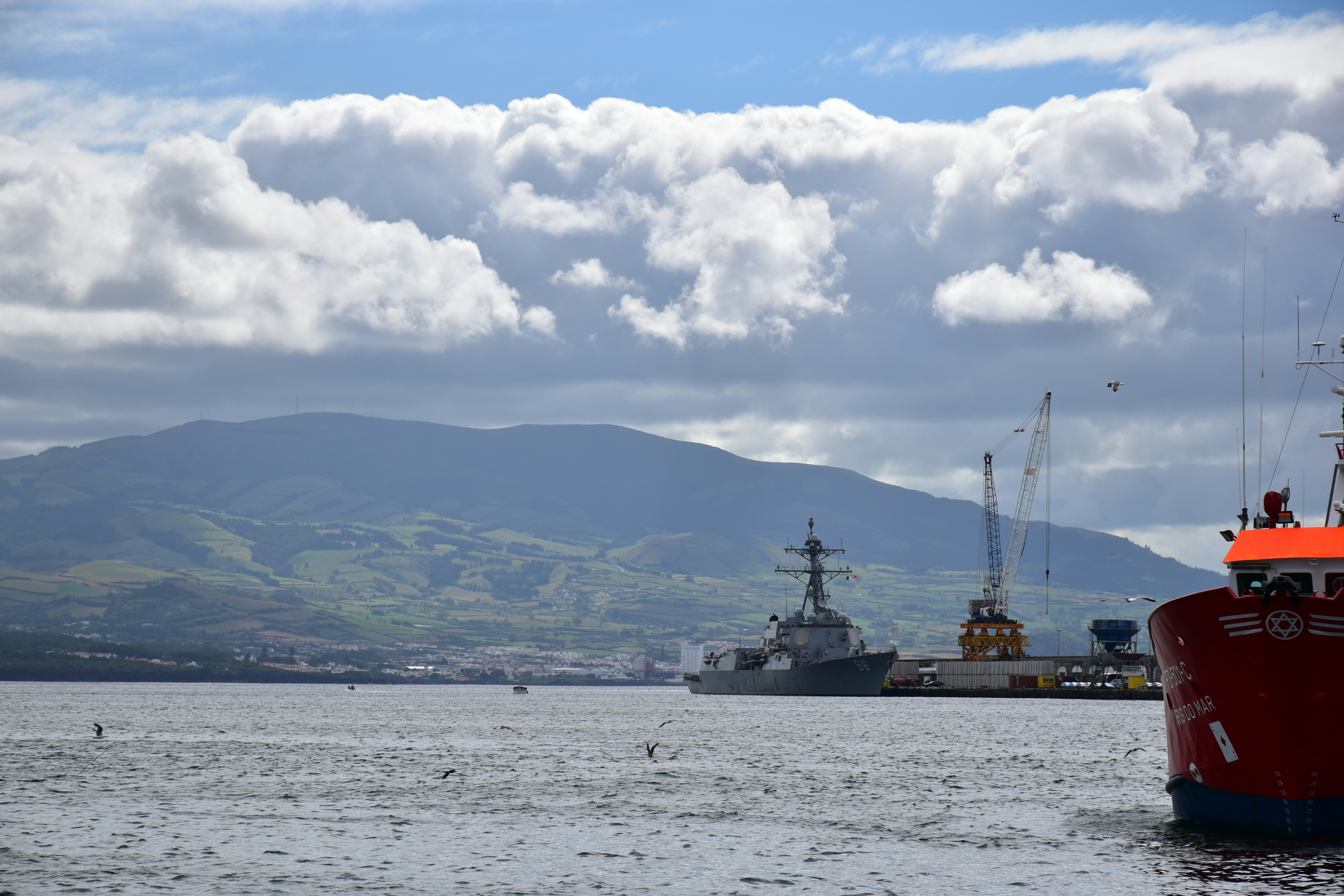 Crimson Hull at the Harbor: Cranes, Clouds, and Open Water