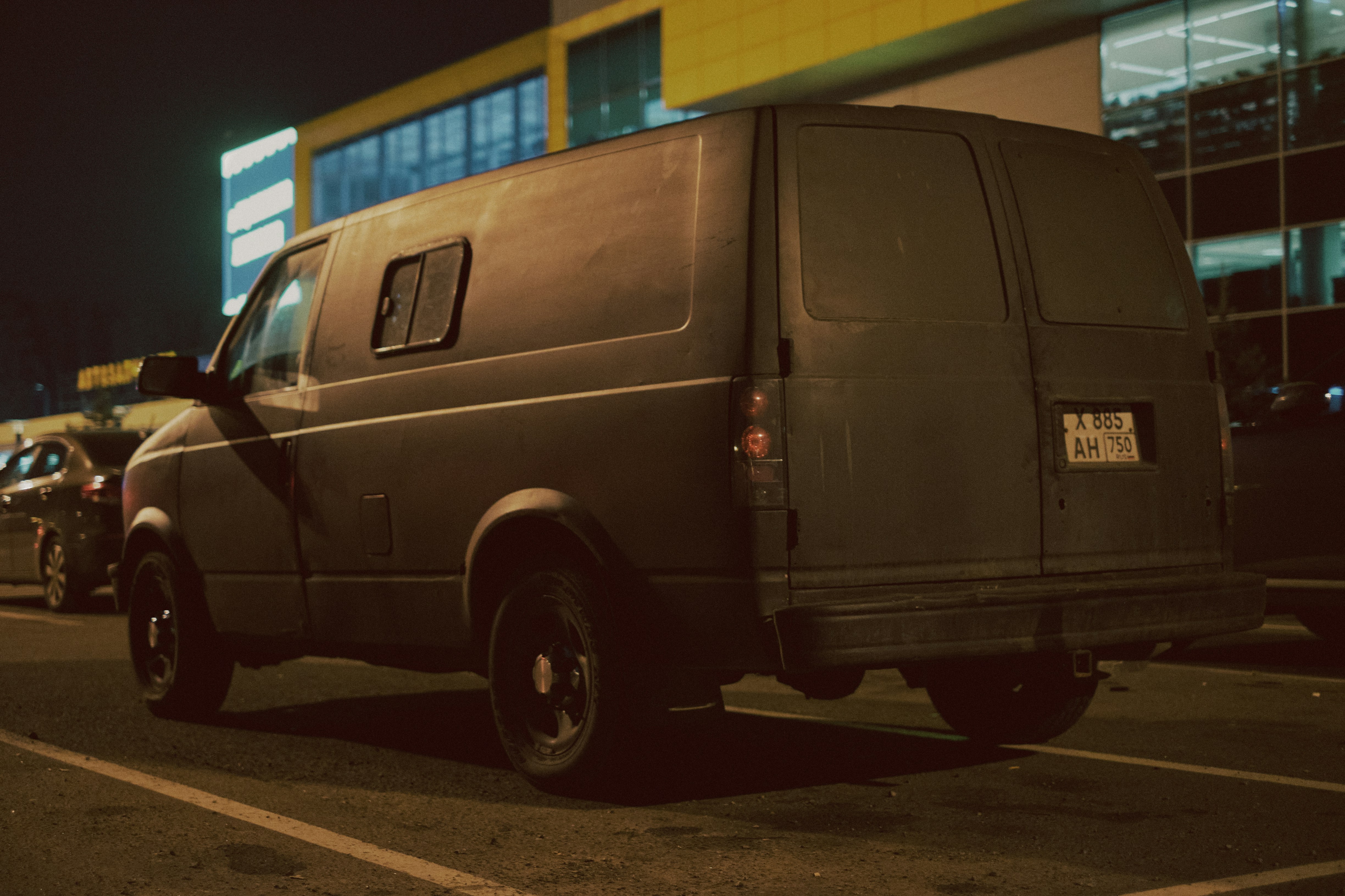 Amber Quiet: A Weathered Van in a Neon-Night Parking Lot