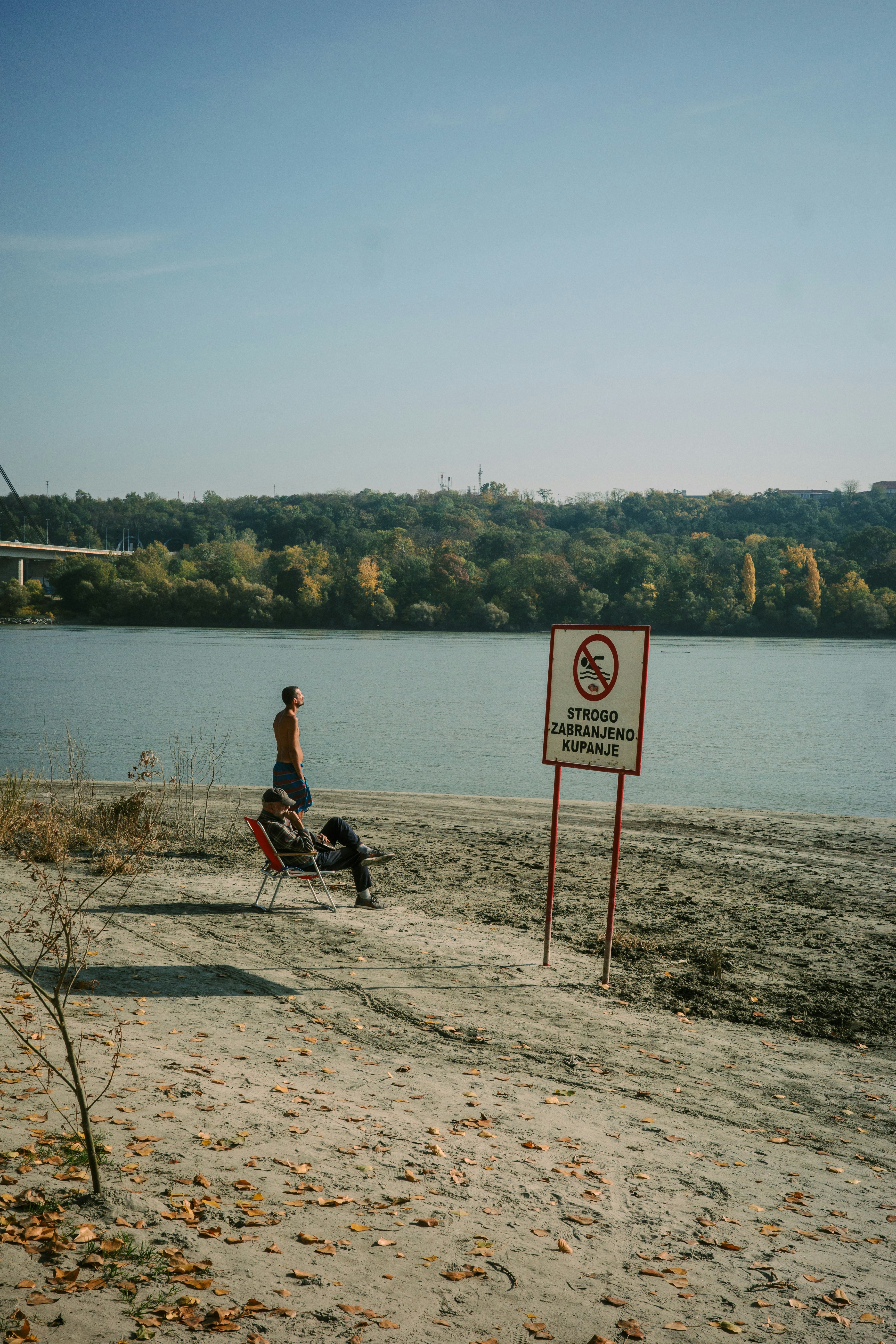 A man walking a dog on a beach next to a river