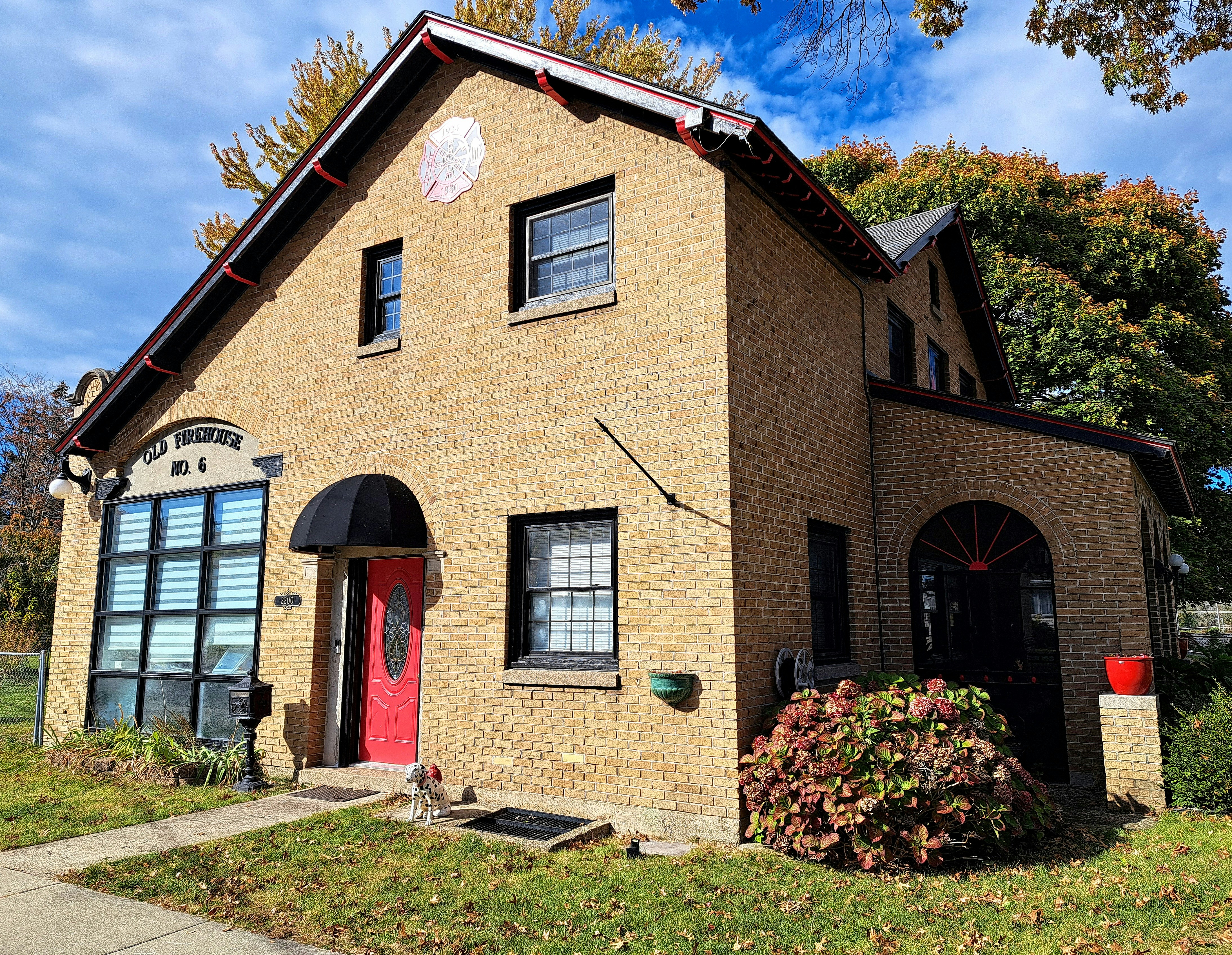 Sunlit Brick Café: Crimson Doorway Amid Autumn Foliage